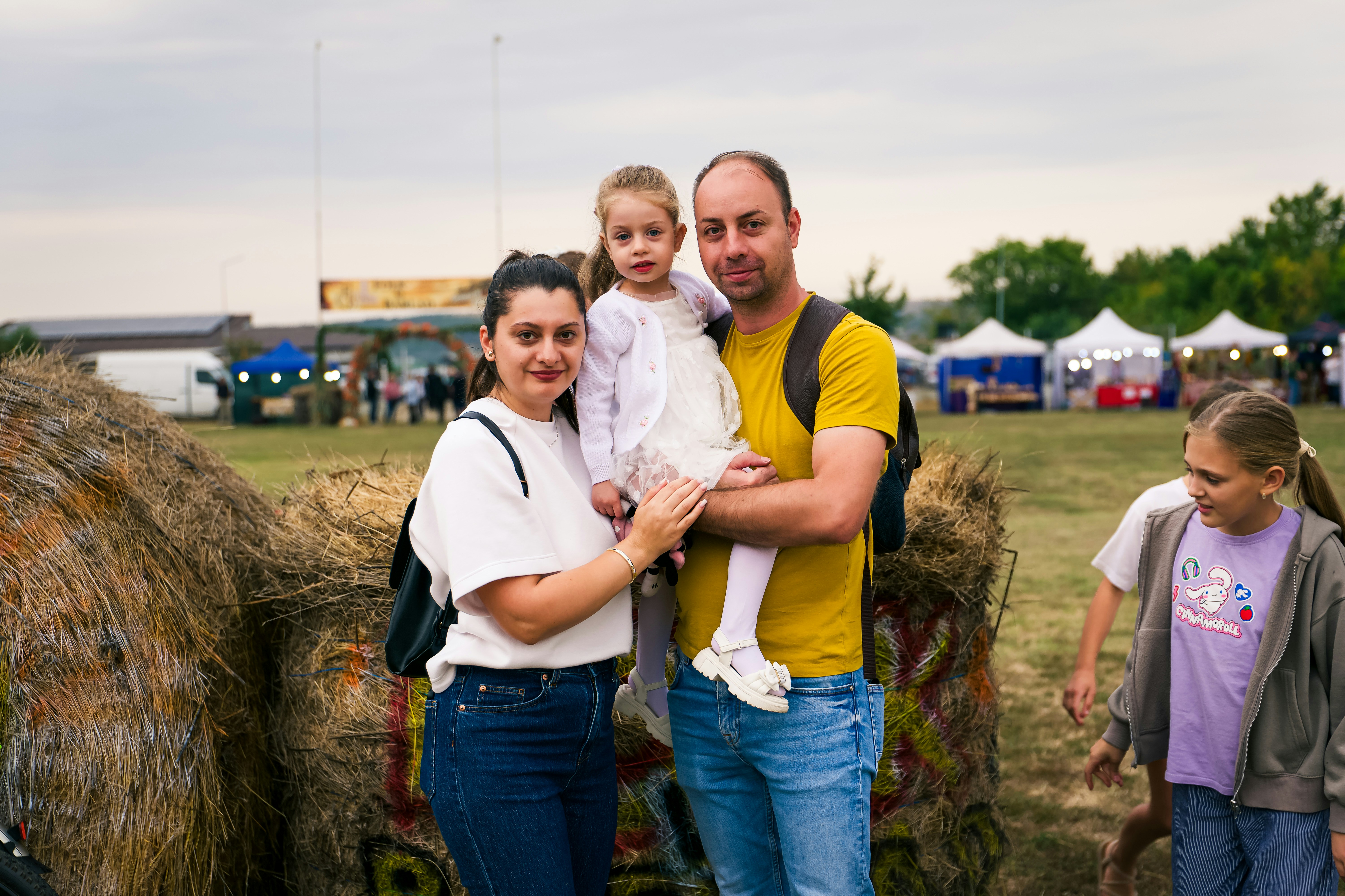 Family at a sunny outdoor fair: central trio with child framed by parents