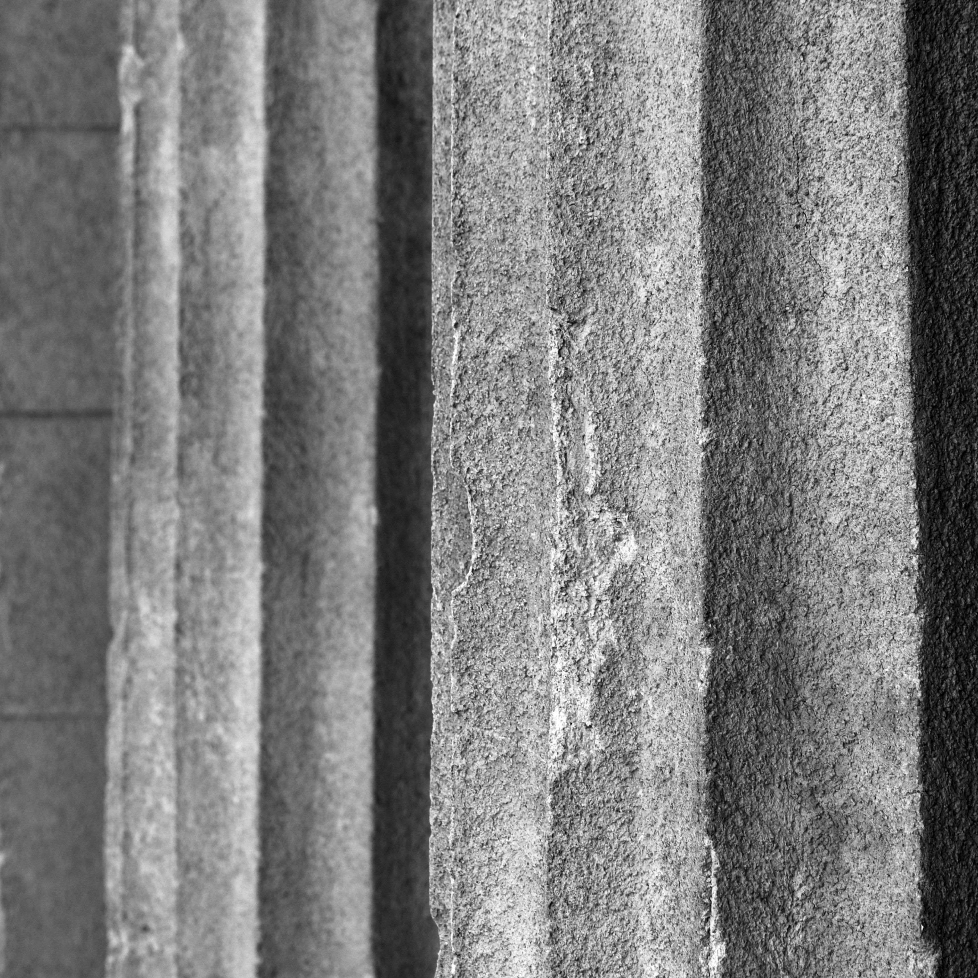 Monochrome close-up of weathered stone pillars standing in a row, emphasizing texture and rhythm of the vertical surfaces.