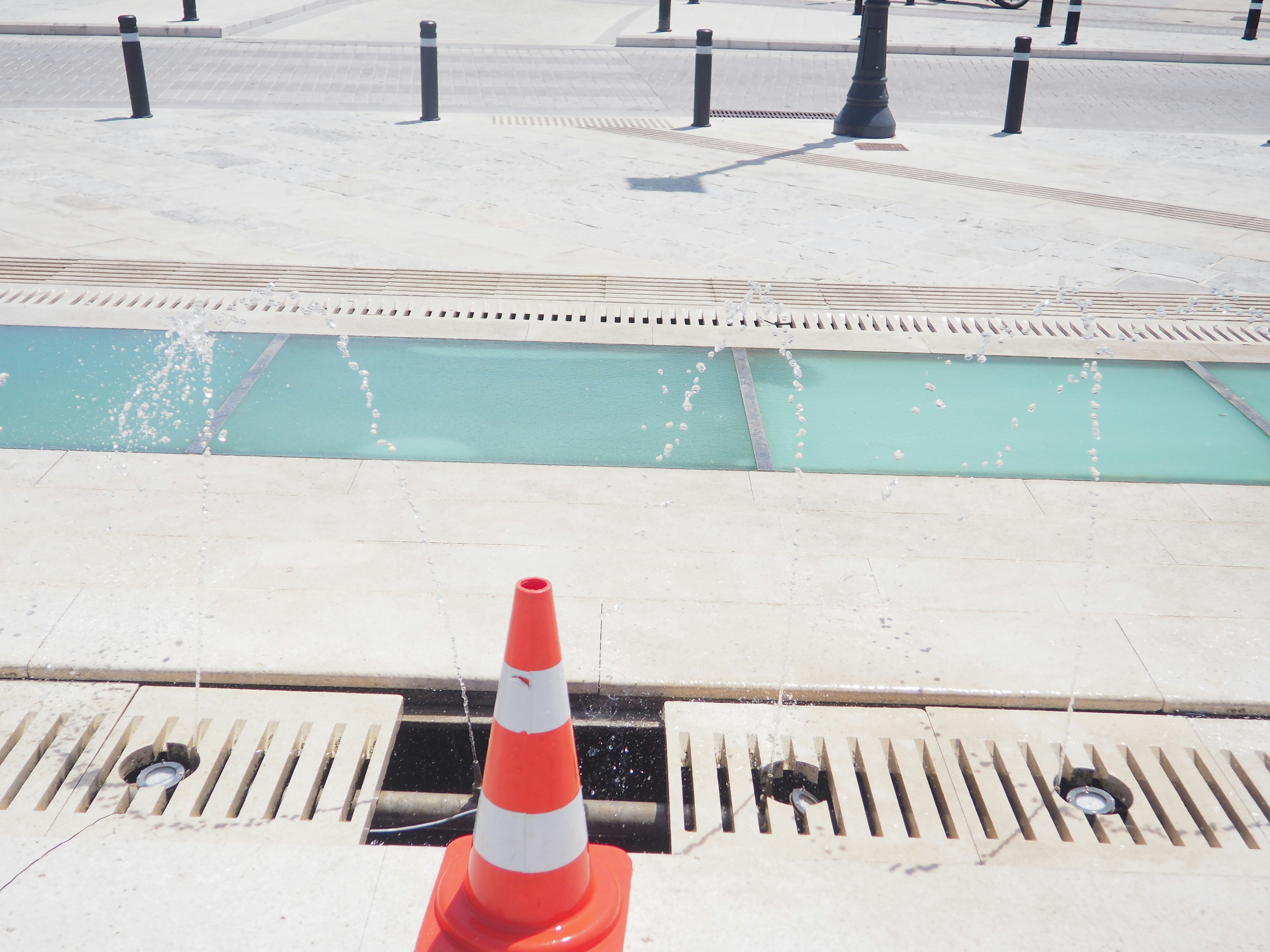 Patterns appear on the road where the lonely traffic cone waits.