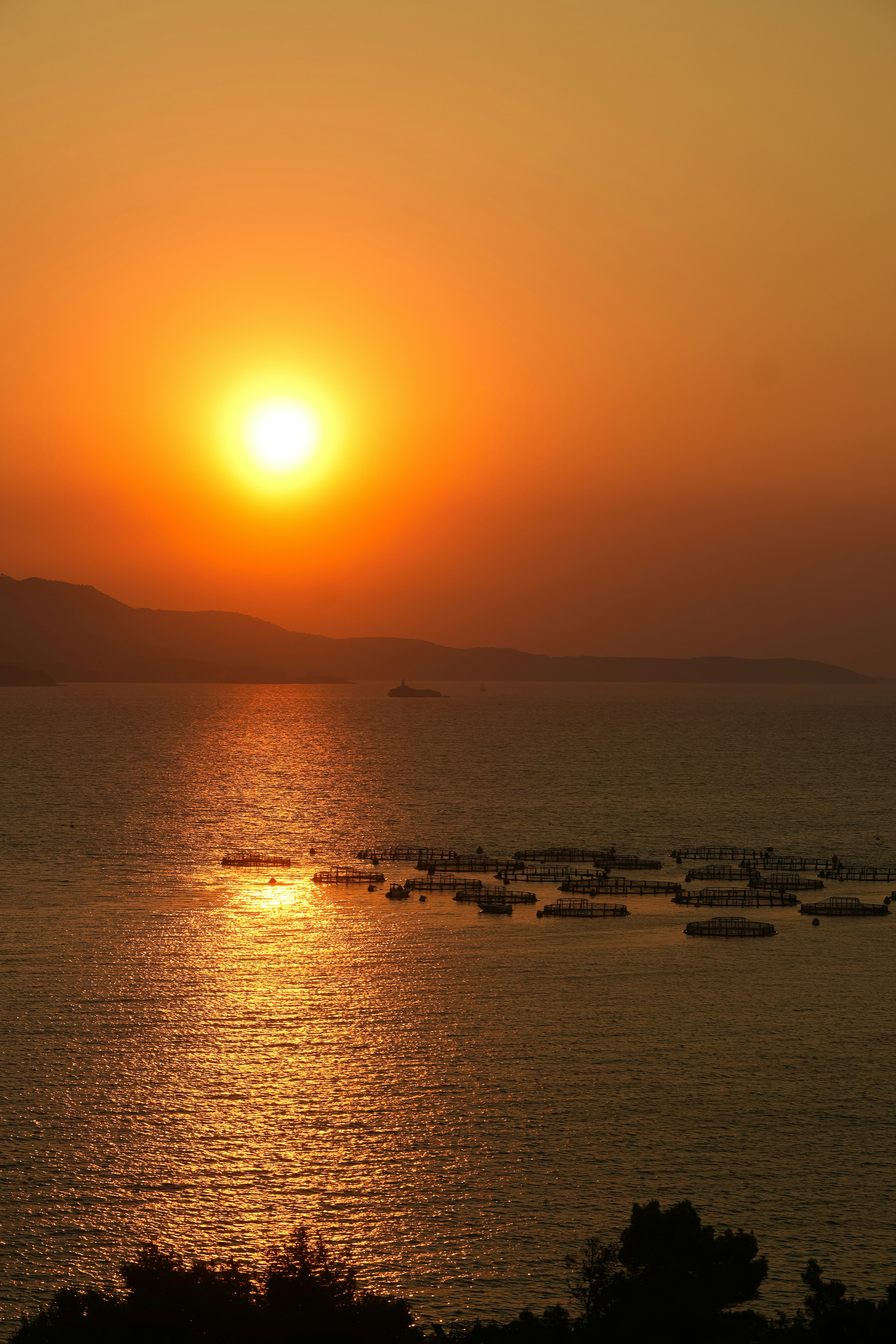 Golden Hour Over Quiet Waters: A Sunset over Boats and Distant Hills
