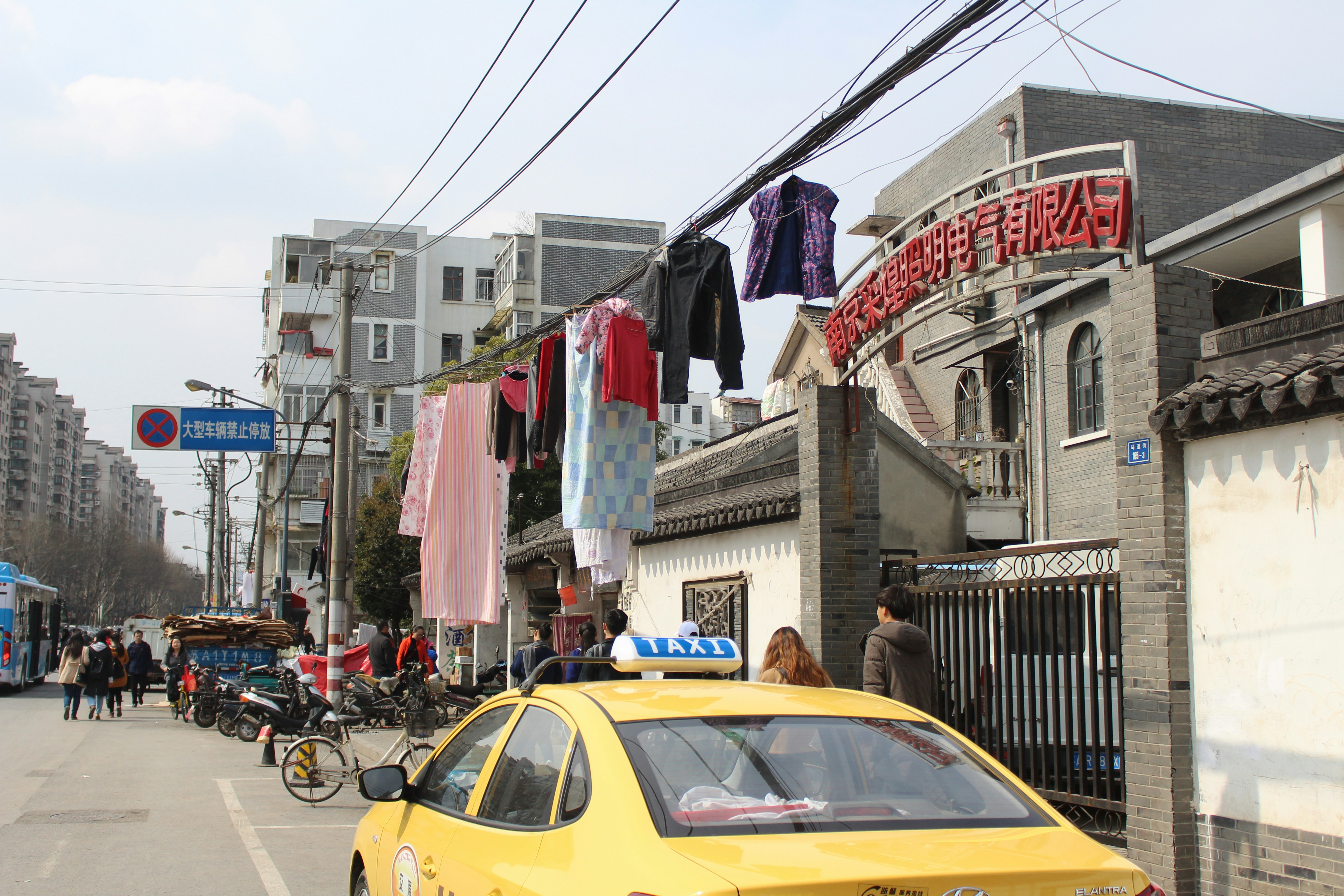 Laundry hanging on lines above a street with a yellow taxi and pedestrians