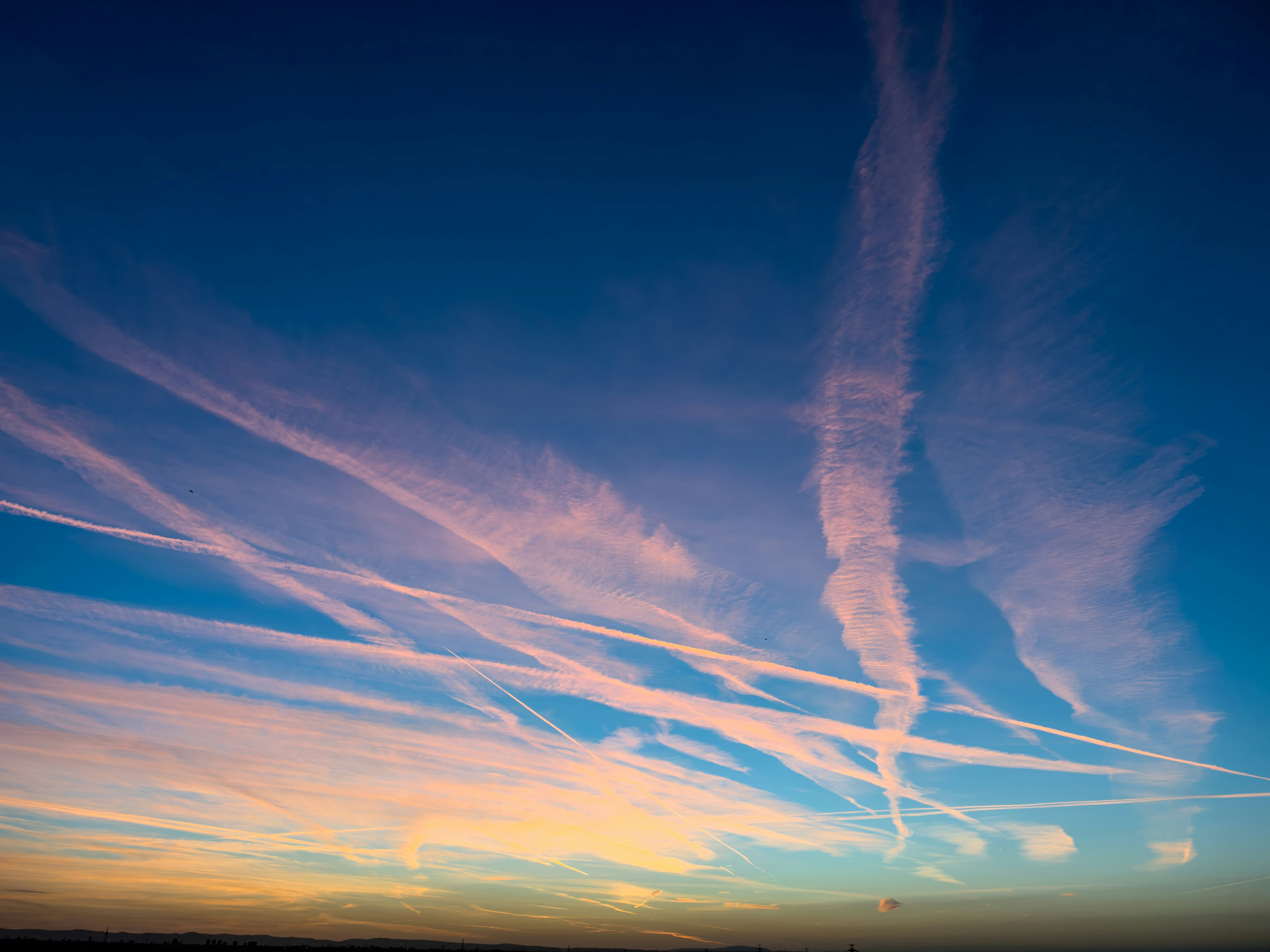 Pink contrails crossing a deep blue sky above a low golden horizon