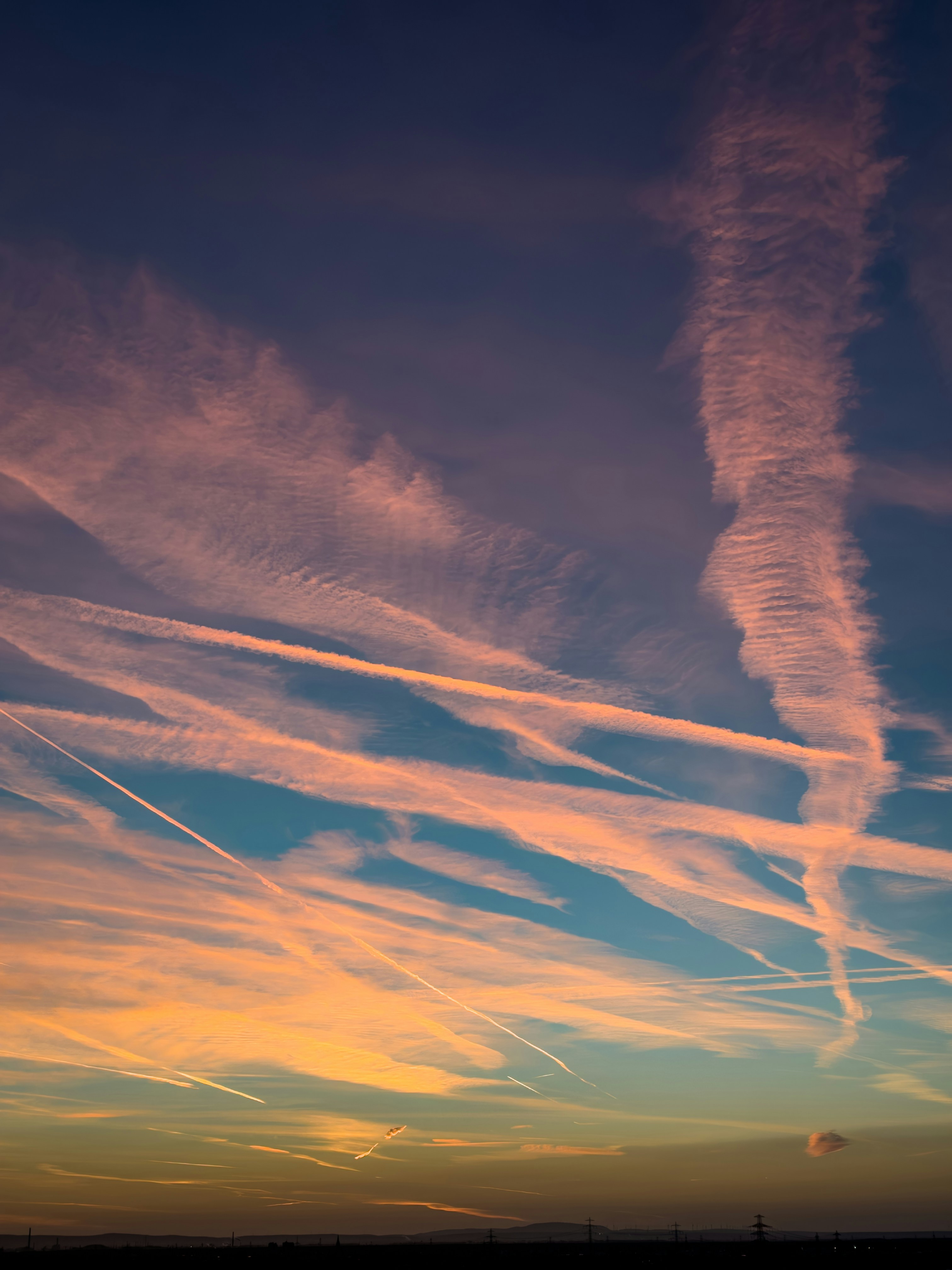 Pink and orange contrails crossing a deep blue sky above a dark horizon