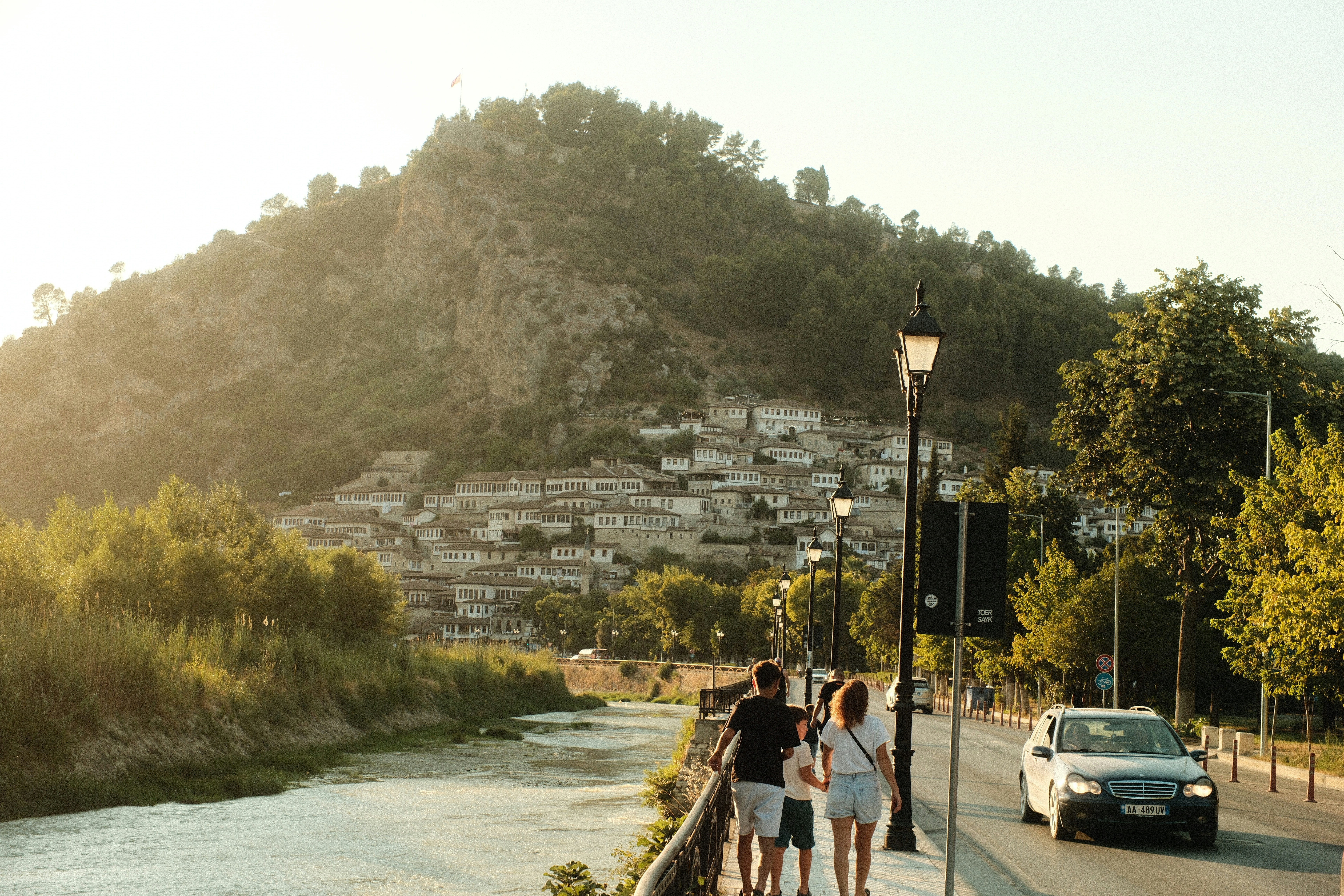 Riverside Promenade at Dusk: A Family Stroll Past a Sunlit Village