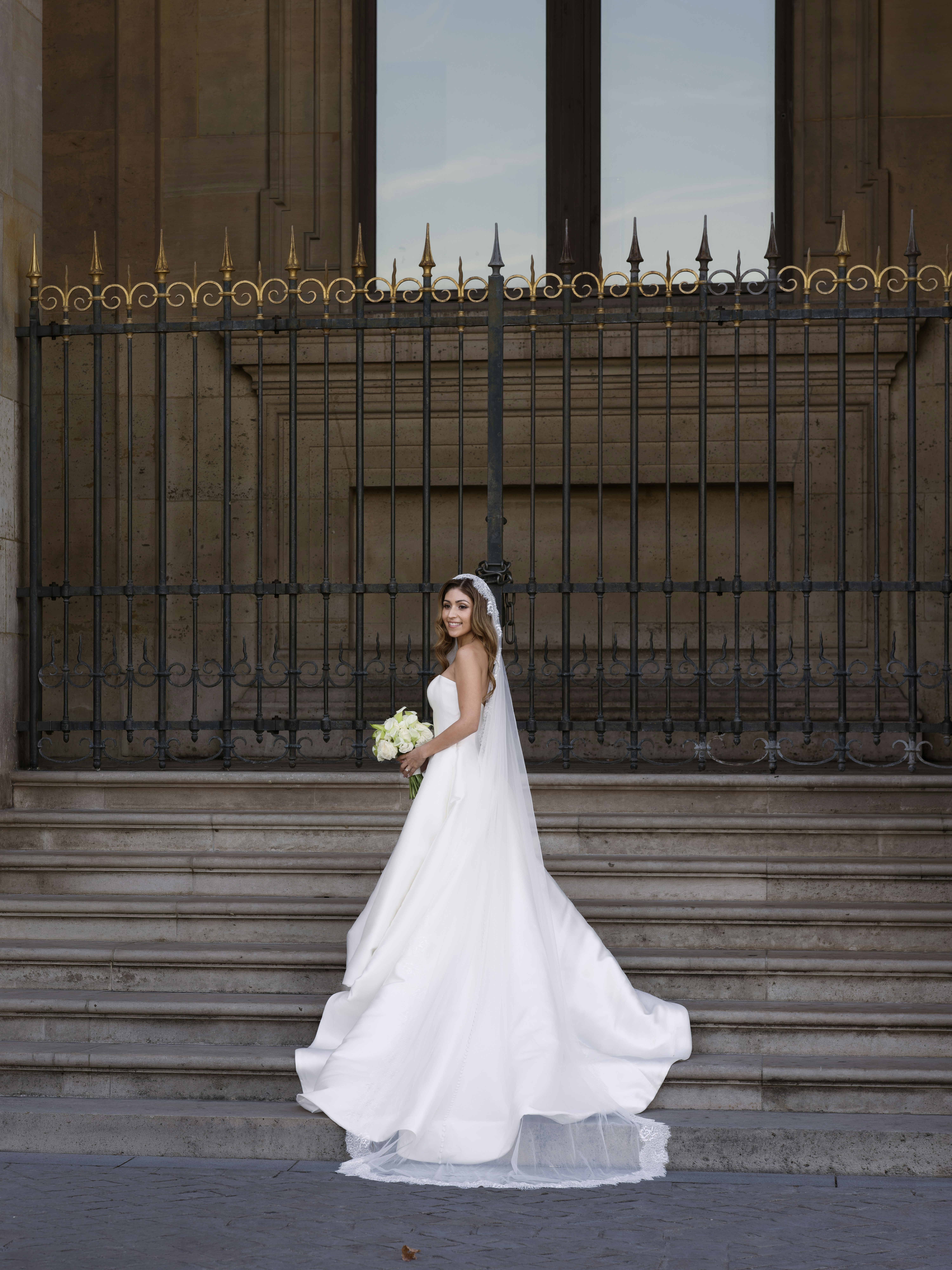 Bride in flowing white gown and bouquet on stone steps