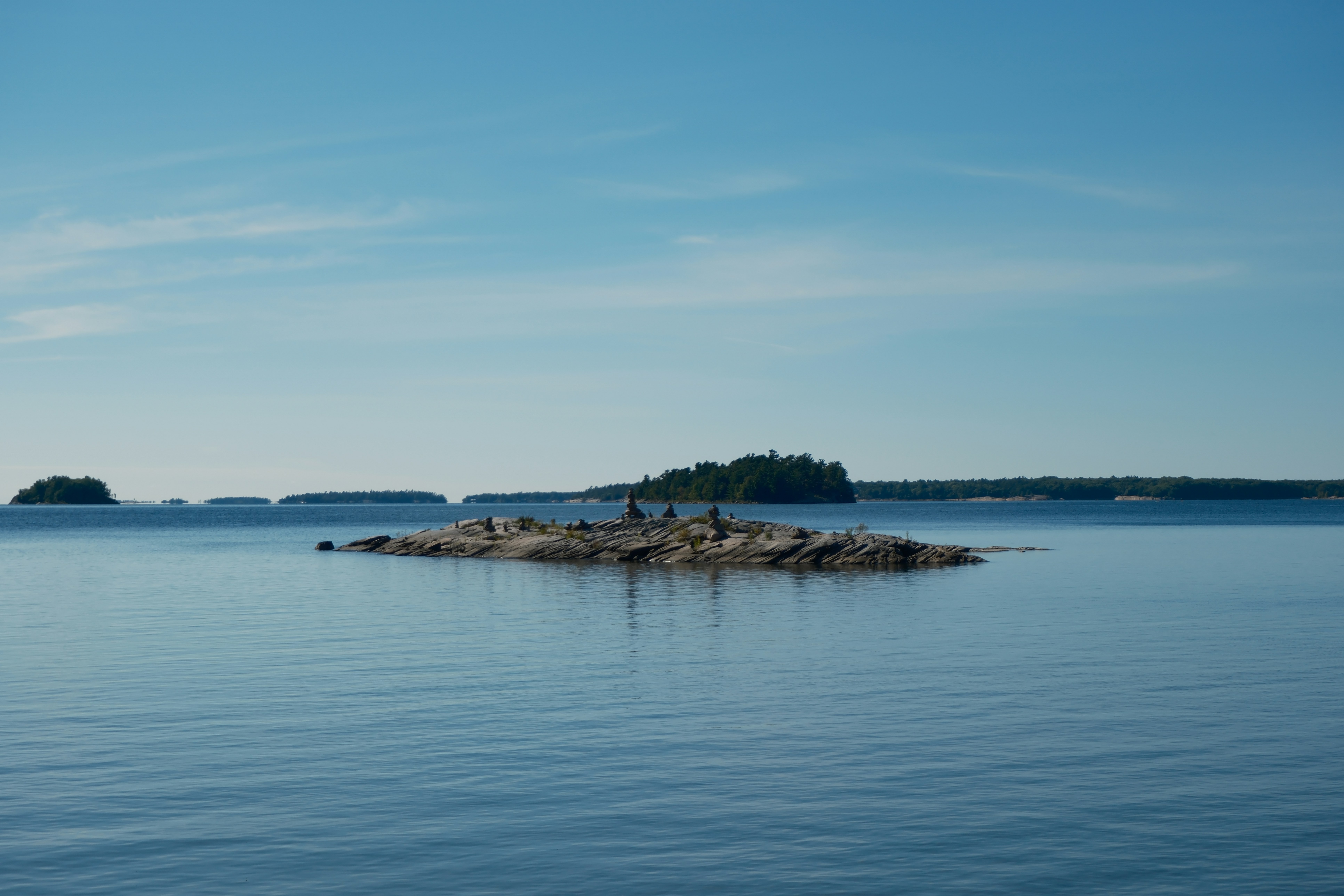 Calm seascape featuring a small rocky outcrop with a cluster of trees in the distance, serene blue water, and a clear sky.