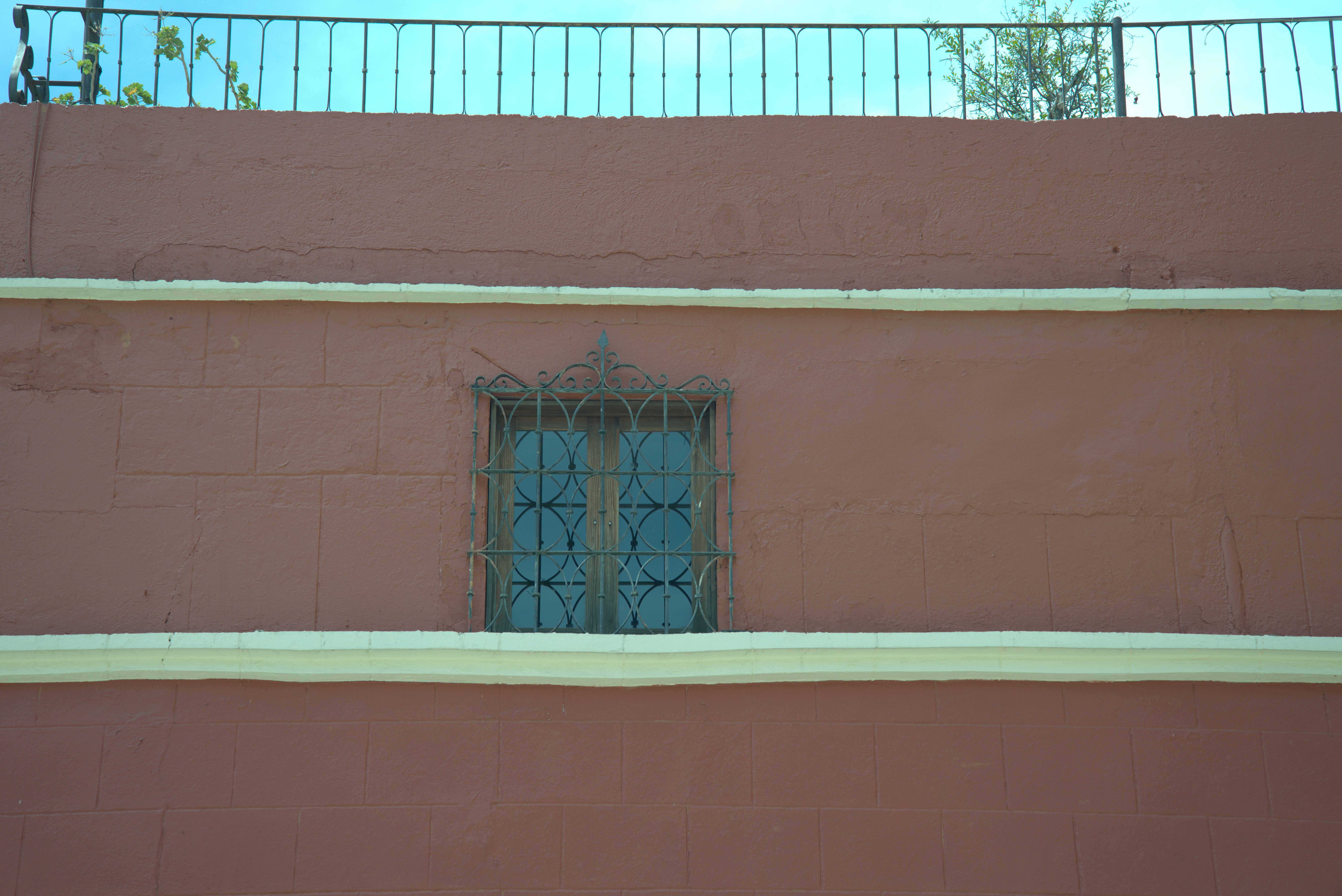 Window in a Deserted Pink Wall Beside a Serrated Fence
