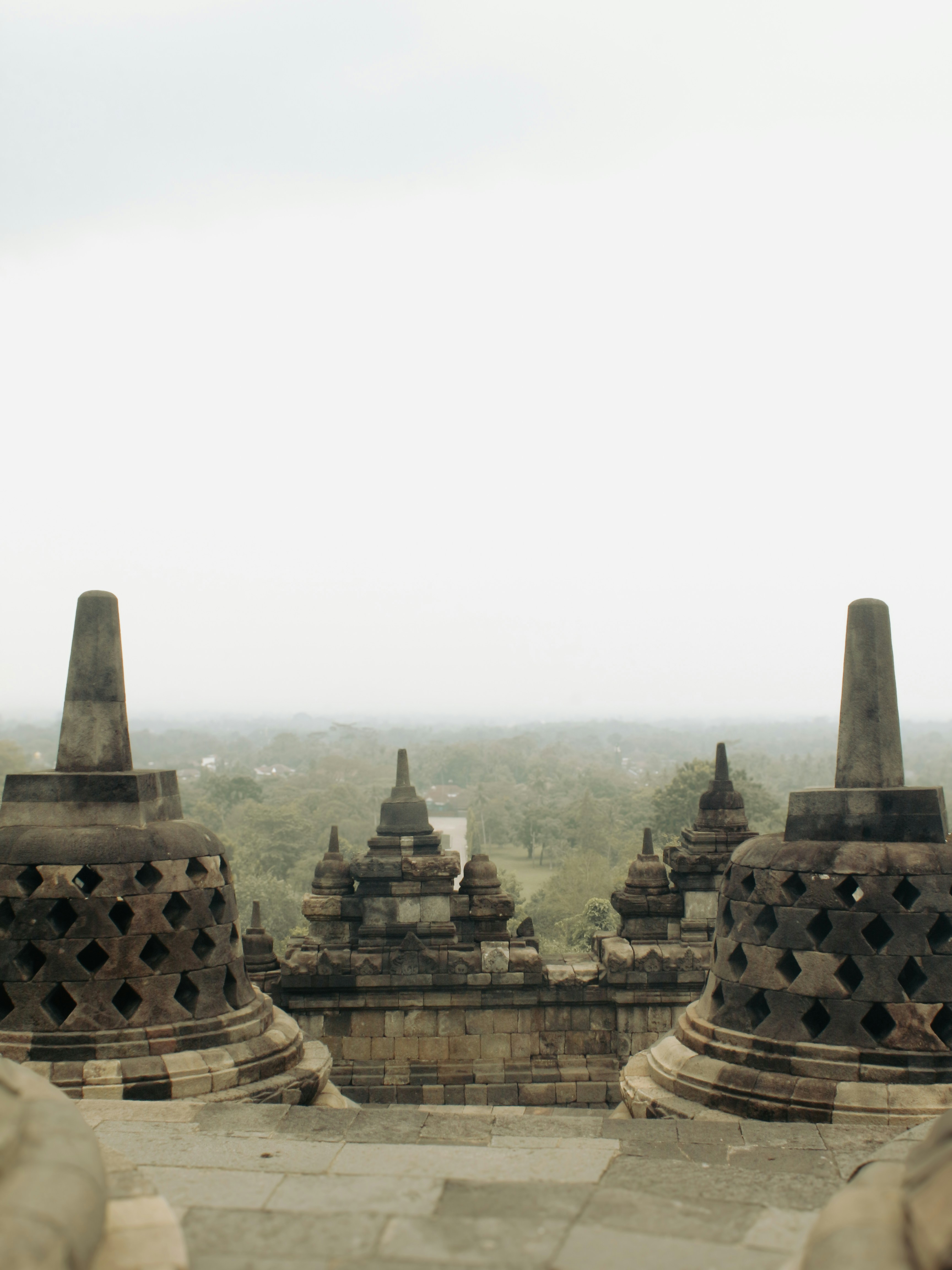 Stone stupas line the foreground with a hazy landscape beyond, evoking a serene view from an ancient temple platform.