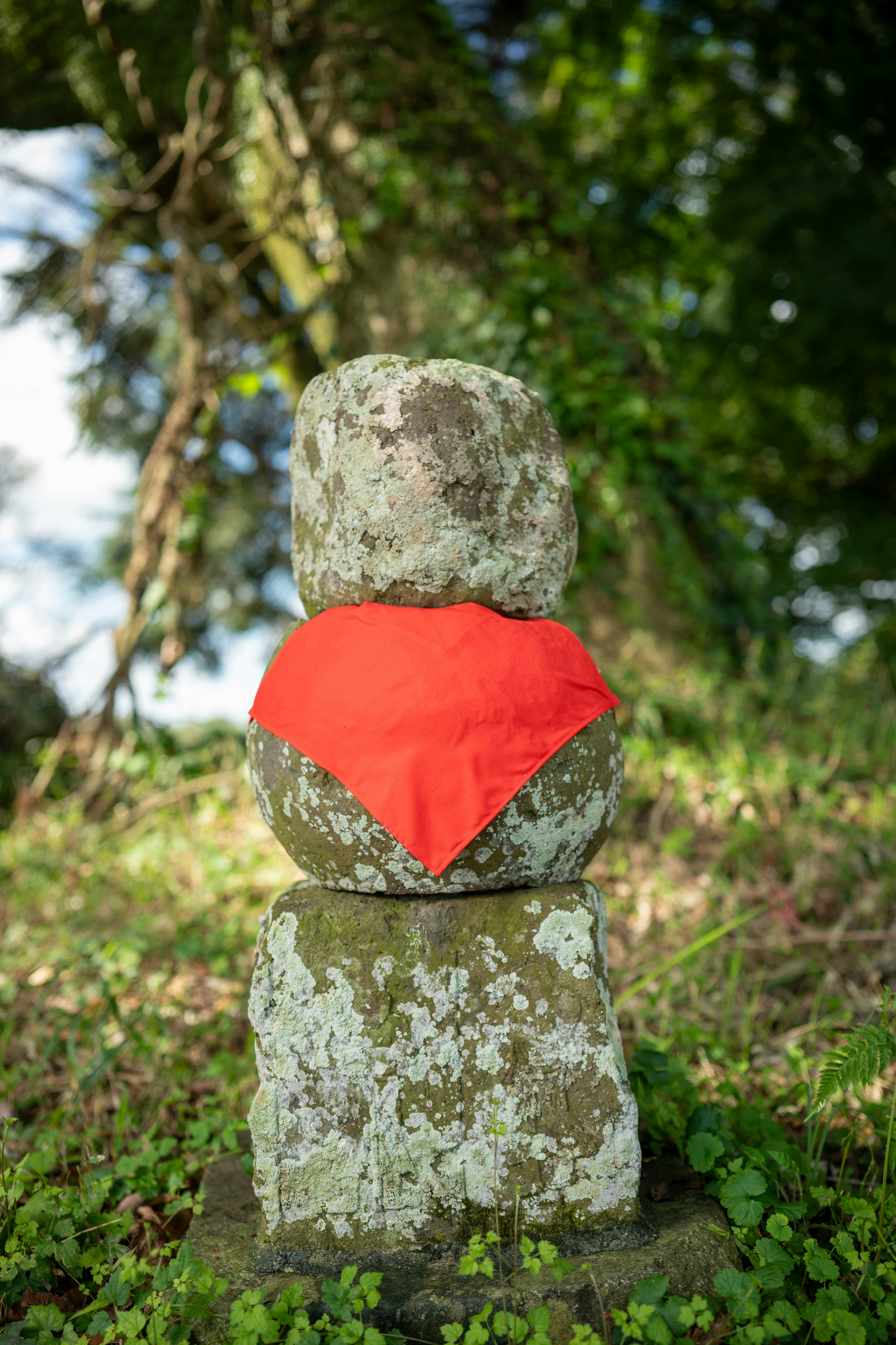 Stone-stack with red cloth cloak in dappled forest light