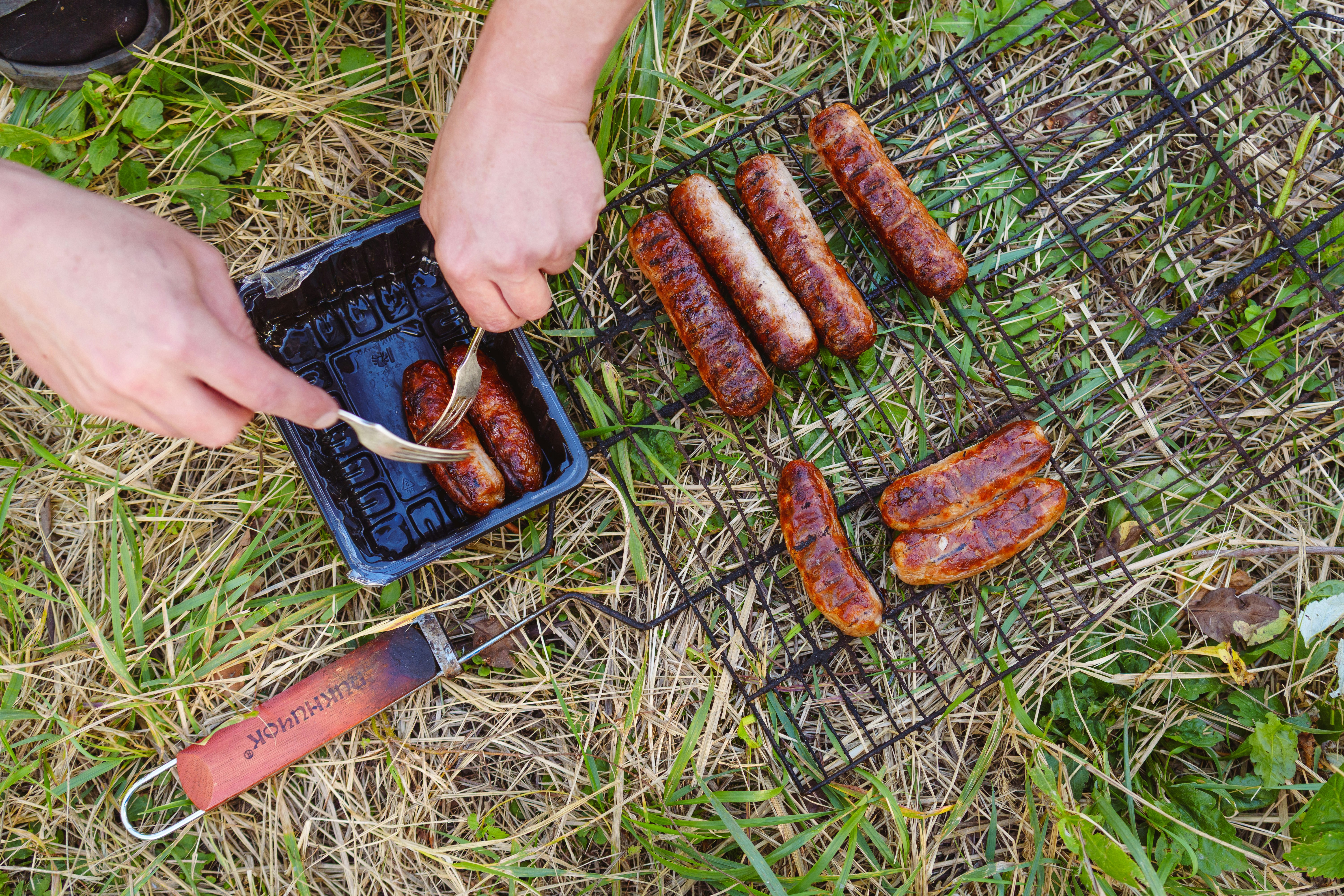 Sizzling sausages on a wire grill over a grassy outdoor setup