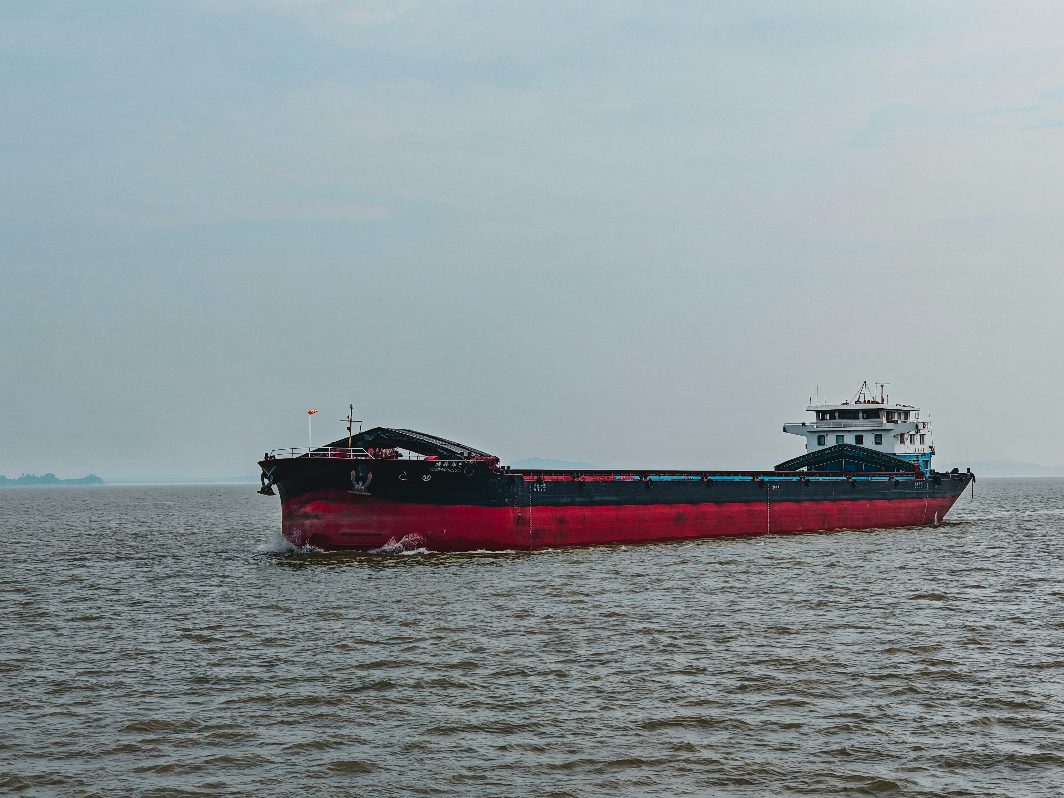 Red-hulled cargo ship gliding across a calm horizon