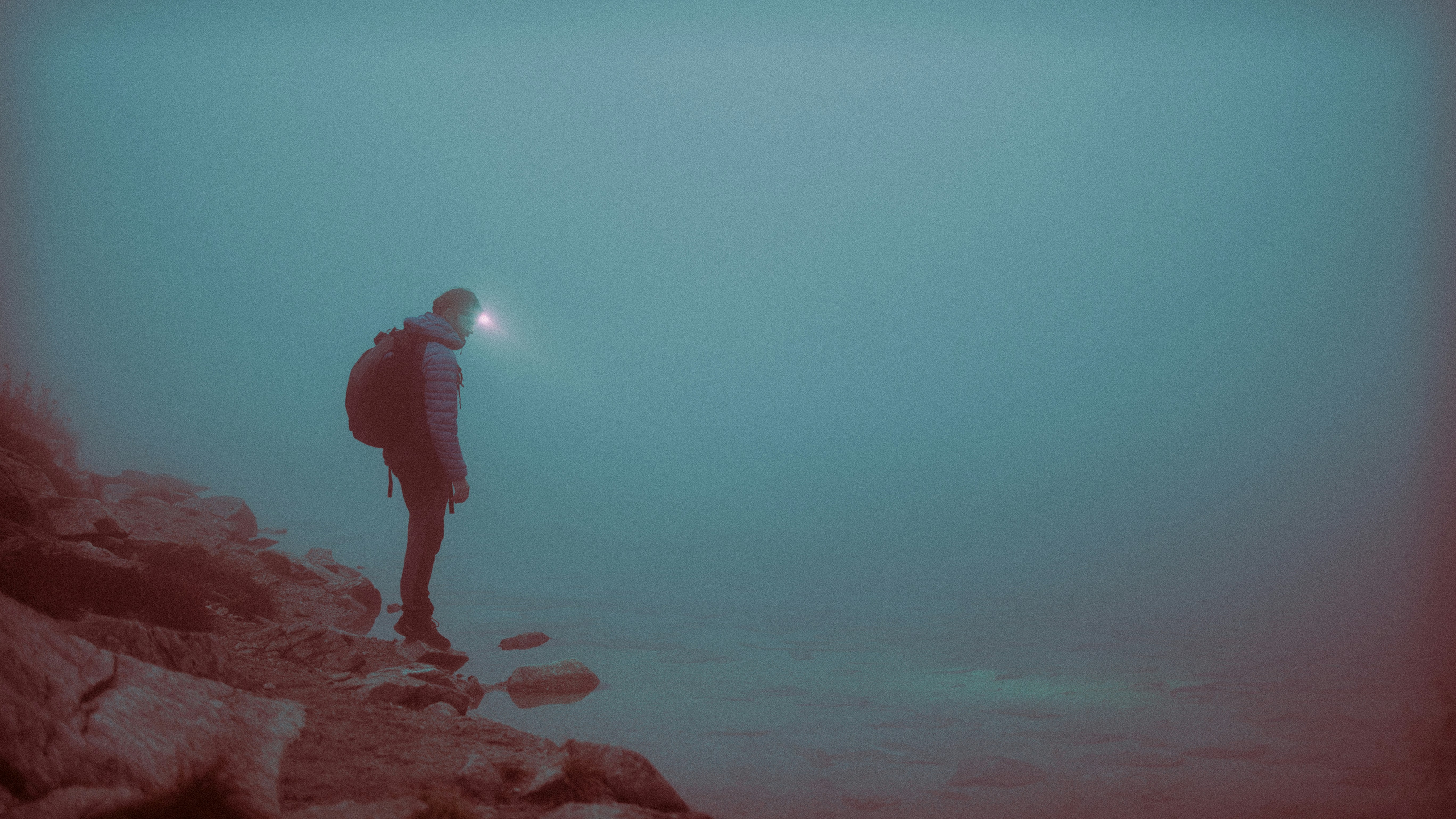 Lantern in the Mist: A Lone Explorer on a Red-tinged Cliff