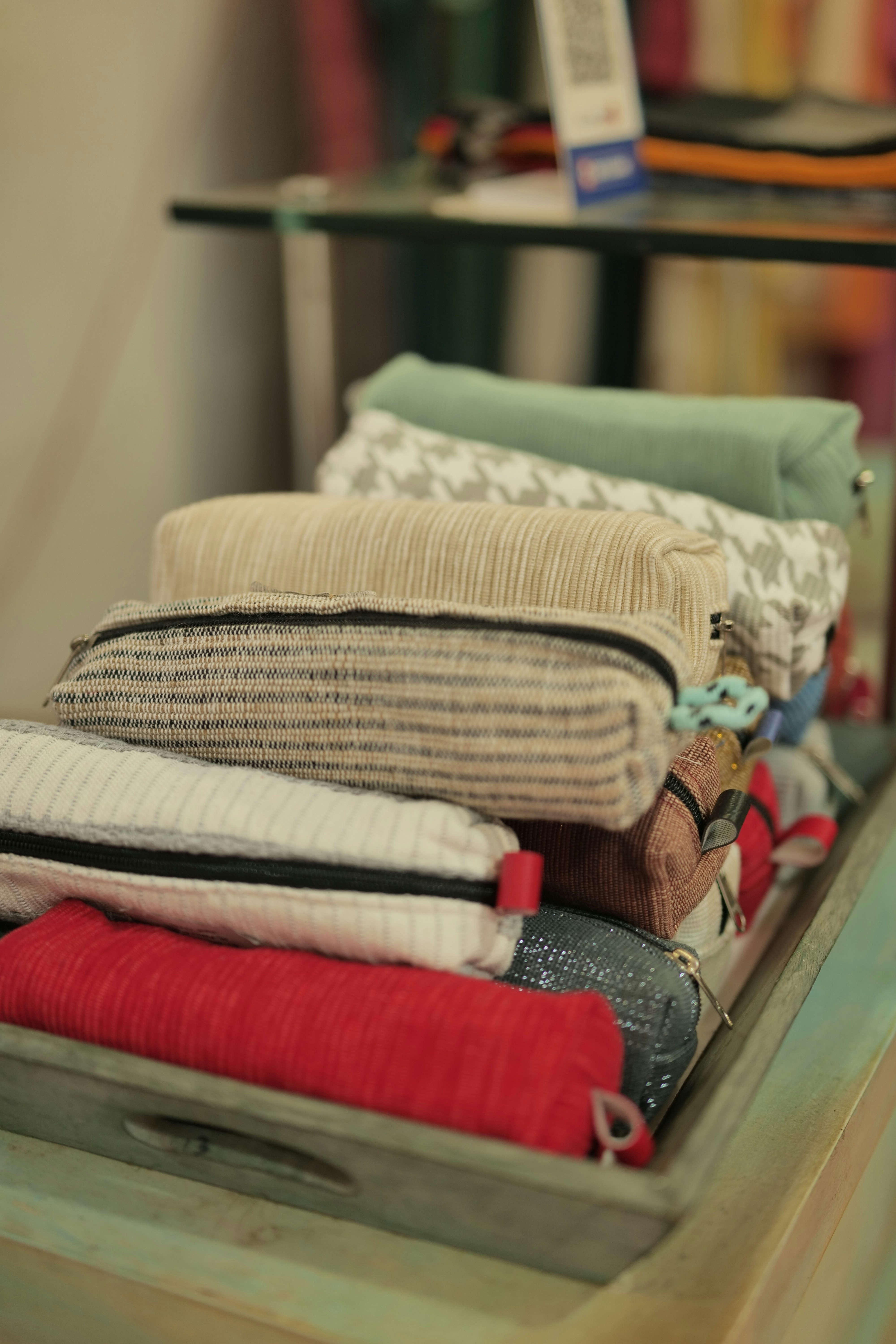 Stacked cosmetic pouches on a glass display with soft focus
