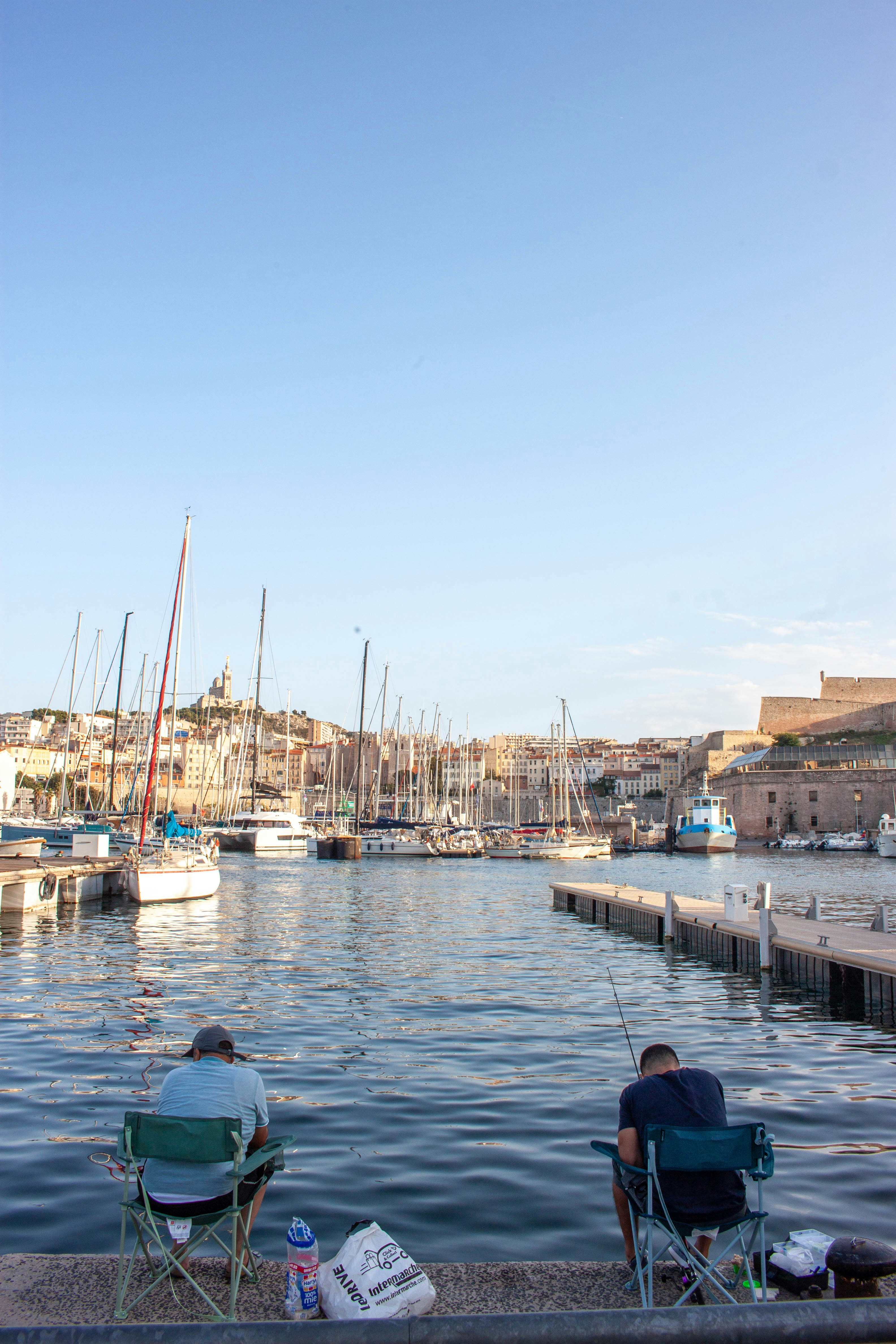 Calm harbor, two anglers at the edge of a sunlit quay