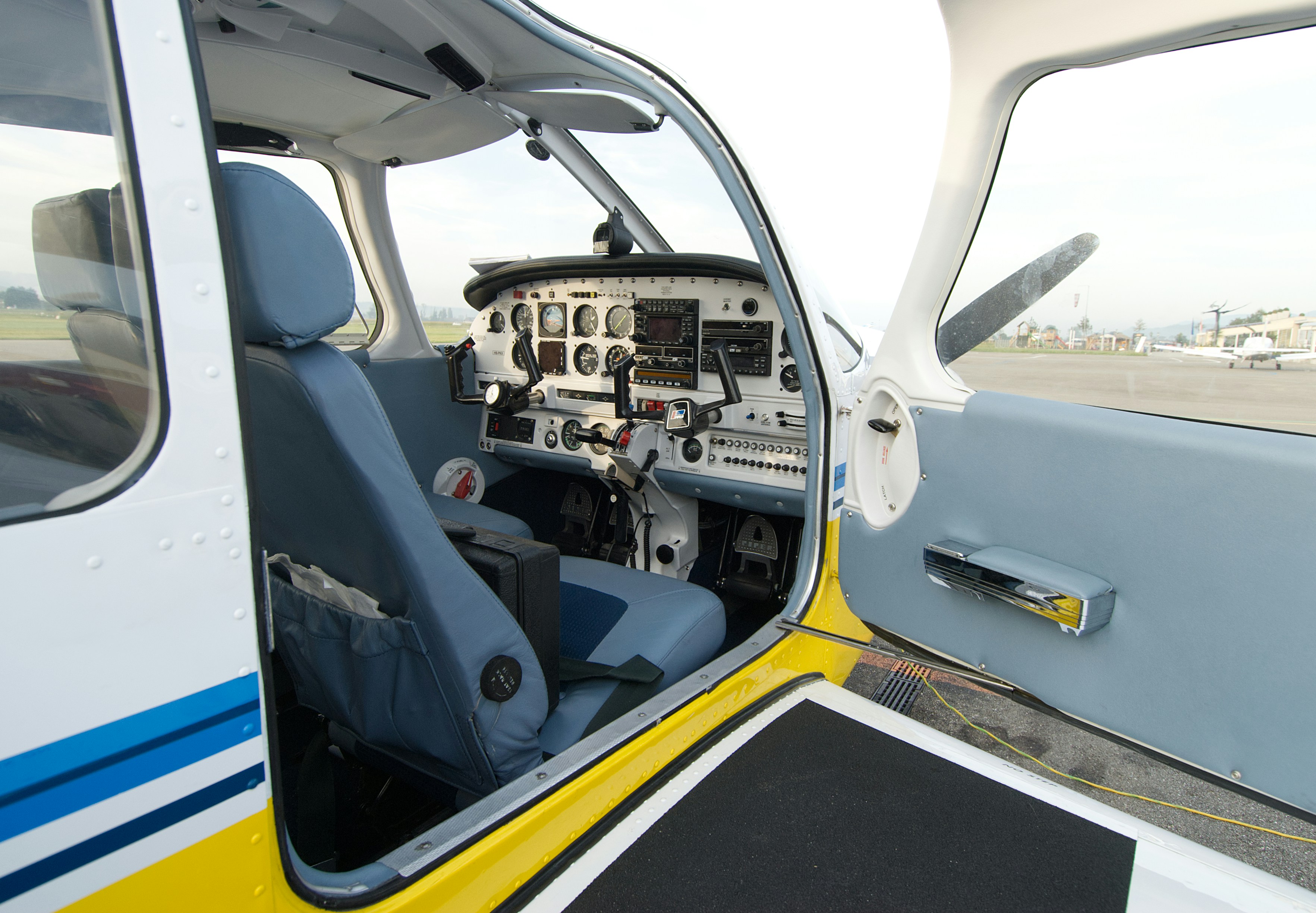 The open cockpit of a small light aircraft with blue seats and instrument panel