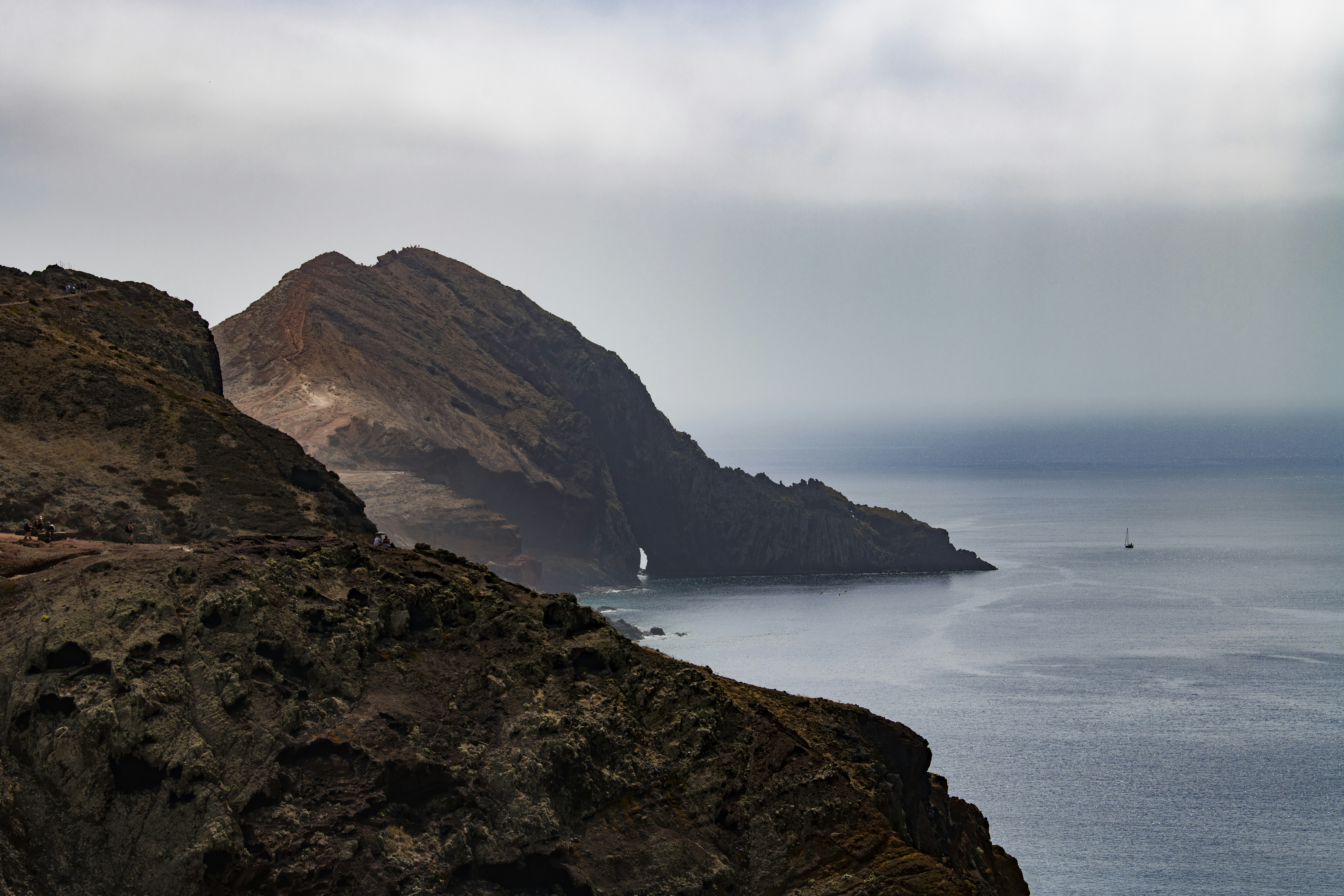 Rugged volcanic cliffs overlooking the ocean under a cloudy sky with a small boat
