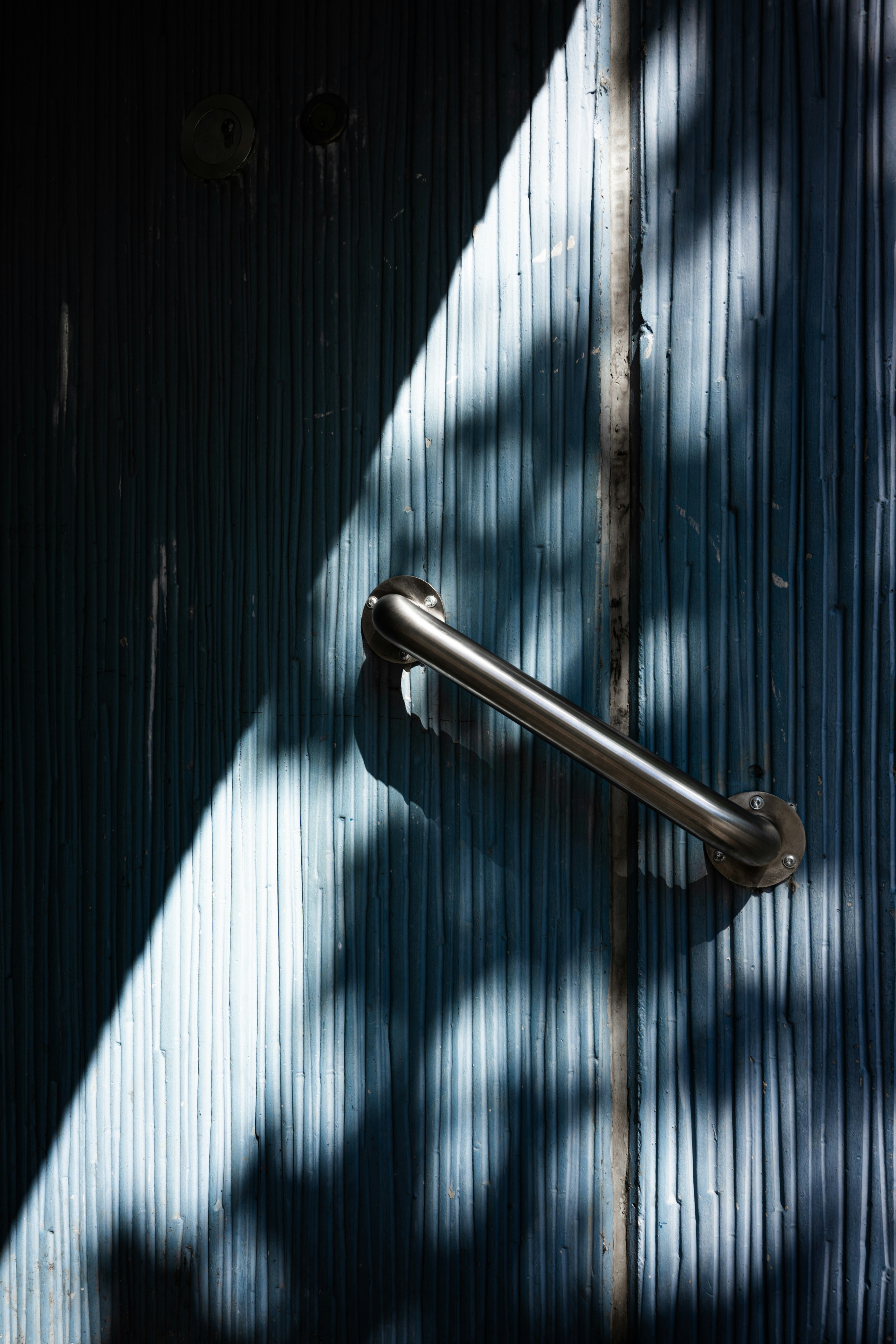Shadowed Handrail: Light Stripes on a Weathered Blue Door