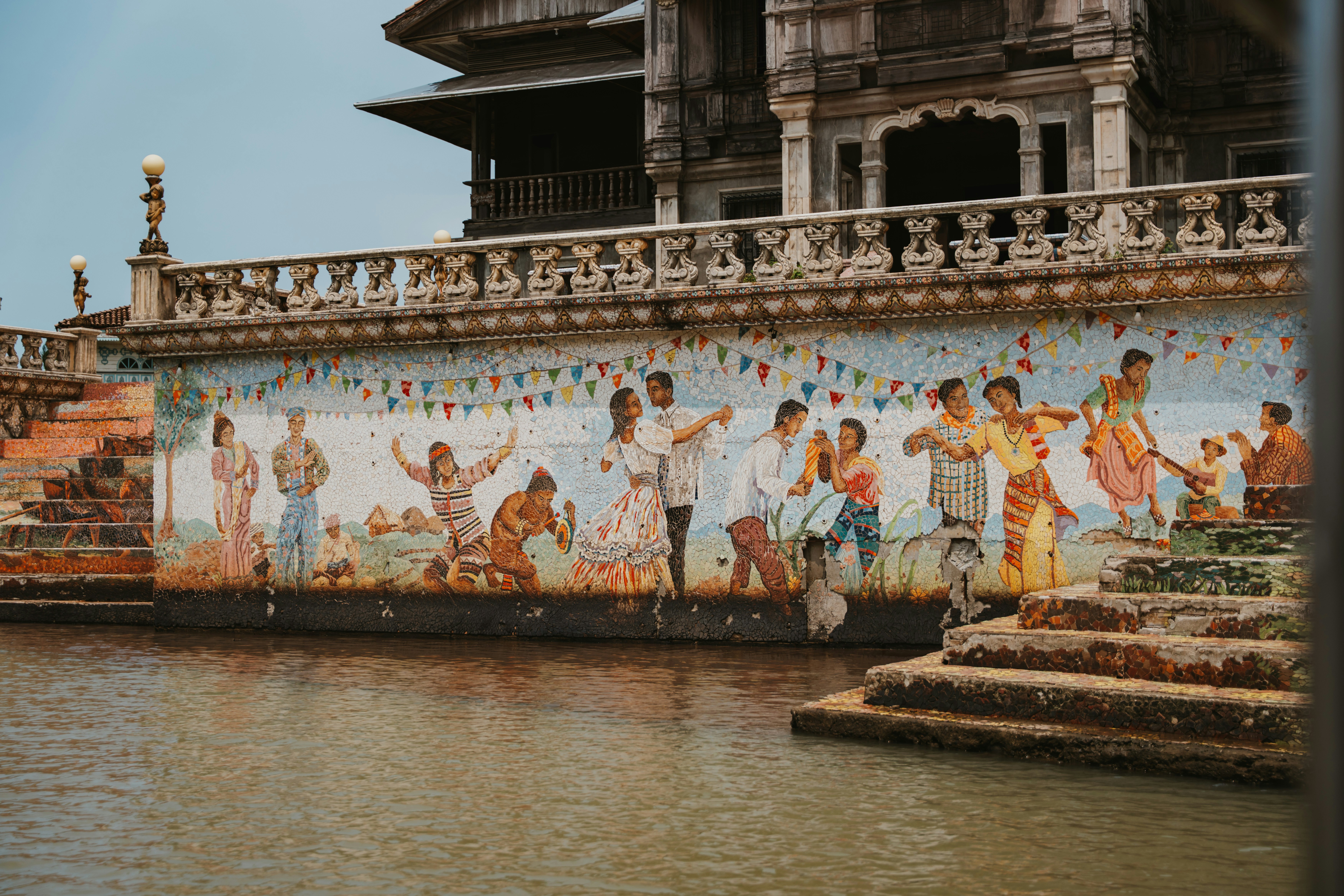 Playful mural by the river: villagers dancing along a painted riverside