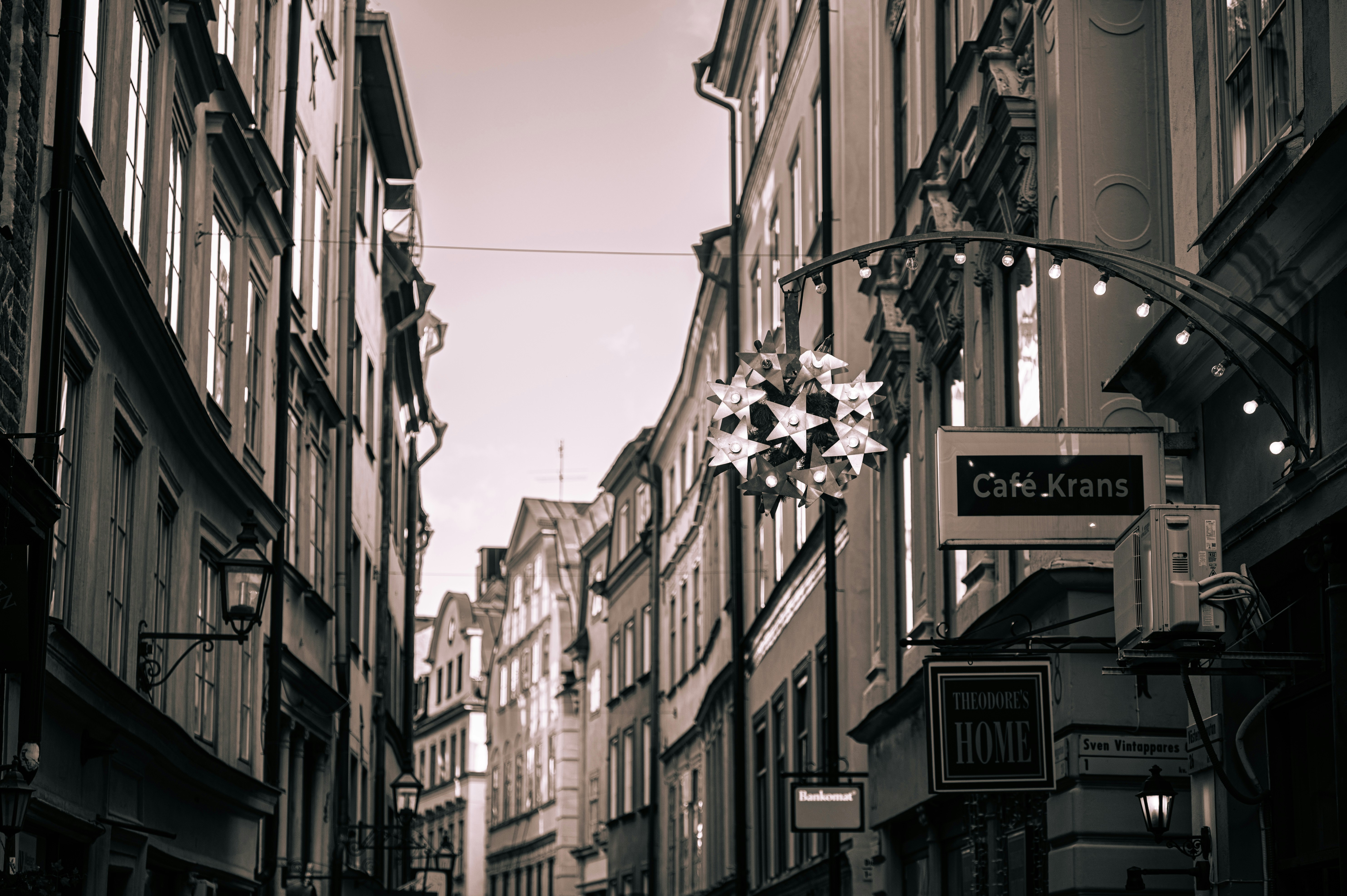 Monochrome street scene with arched buildings and festive star lanterns hanging above a narrow alleyway, capturing urban charm and seasonal decor.