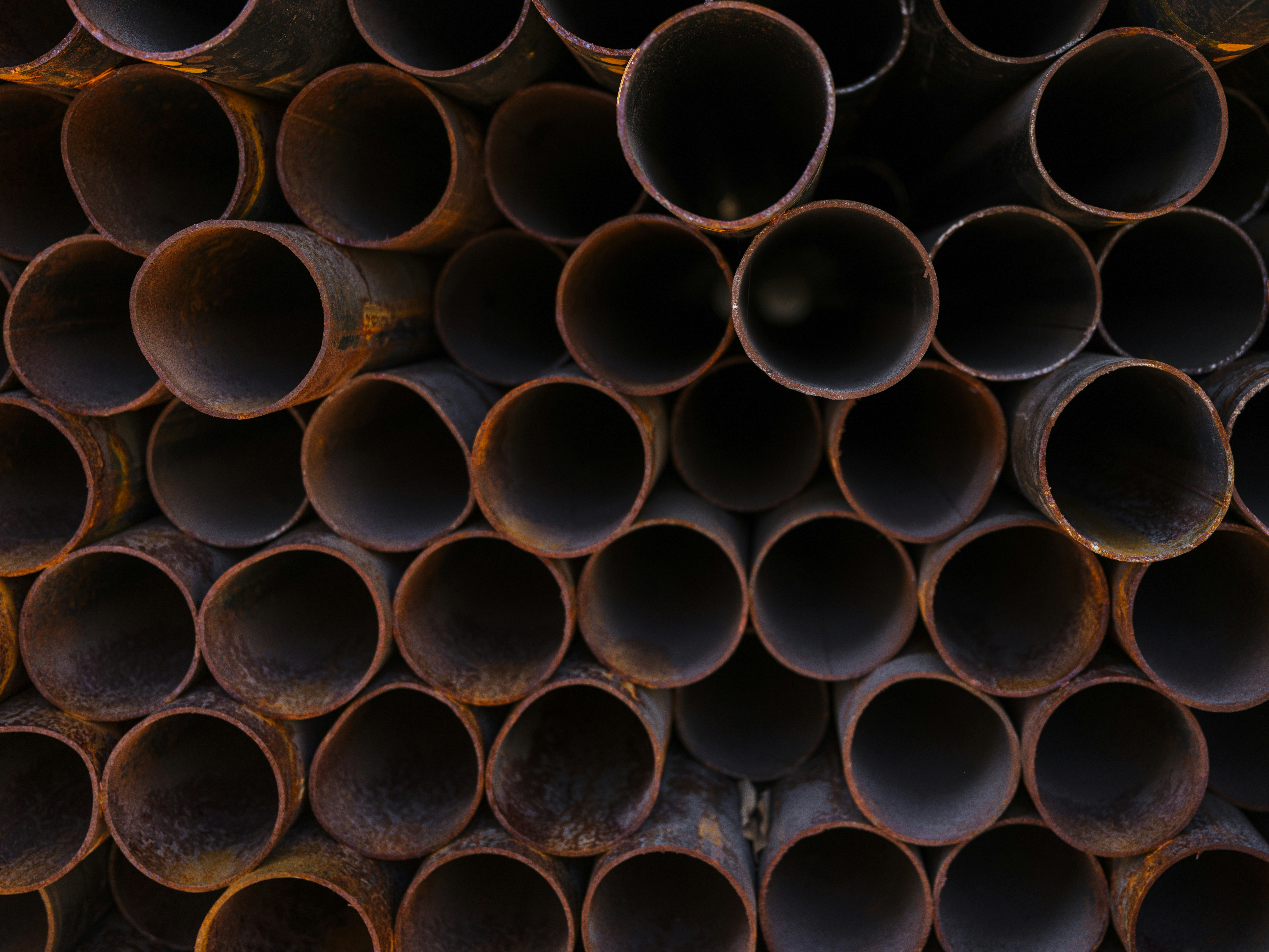 Dense stack of rusted metal pipes viewed head-on, forming circular rims with dark interiors; industrial texture emphasizes repetition and depth.
