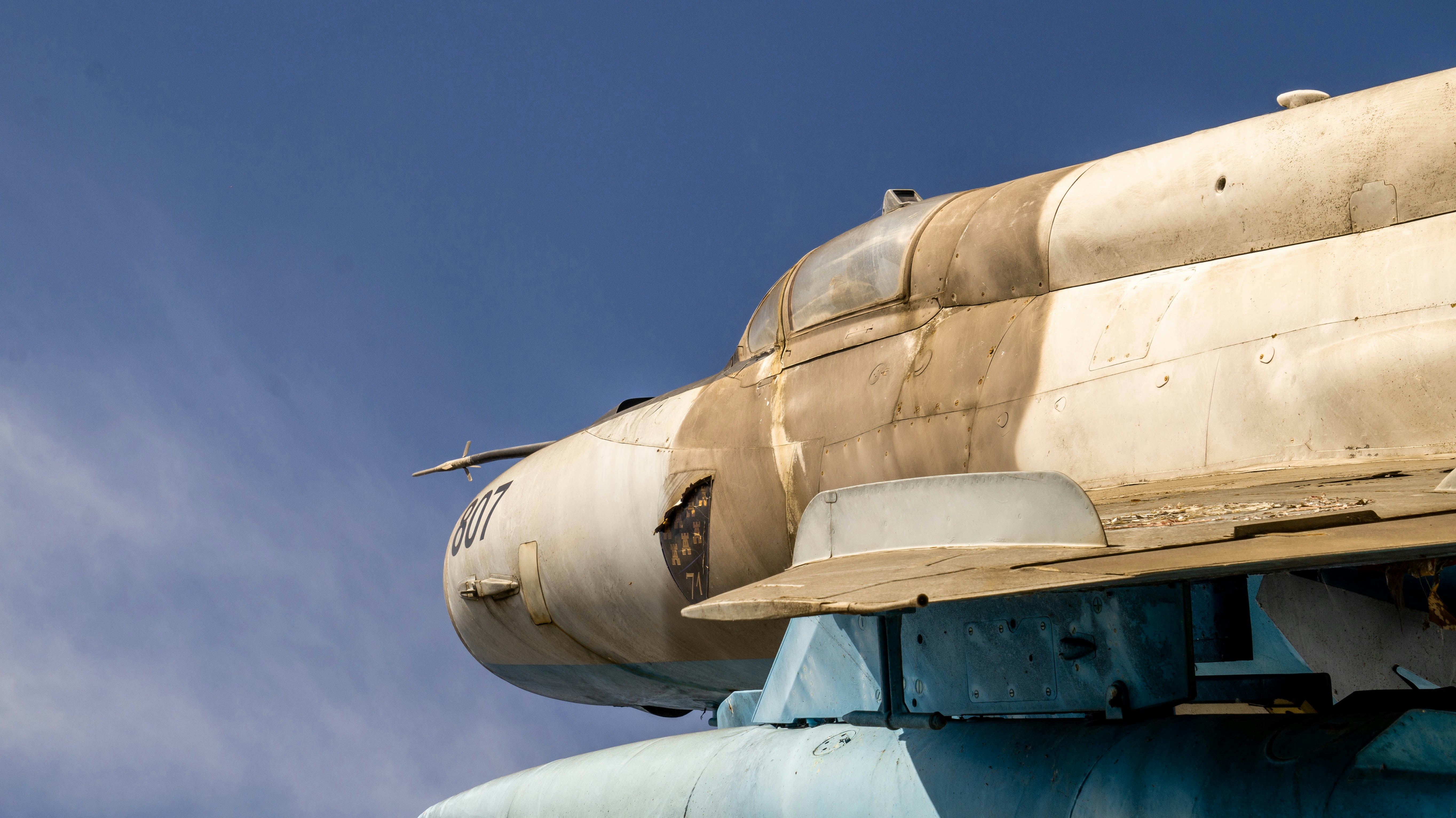 A close-up of a weathered vintage jet fuselage against a clear blue sky, emphasizing the worn surfaces and muted tones of the aircraft.