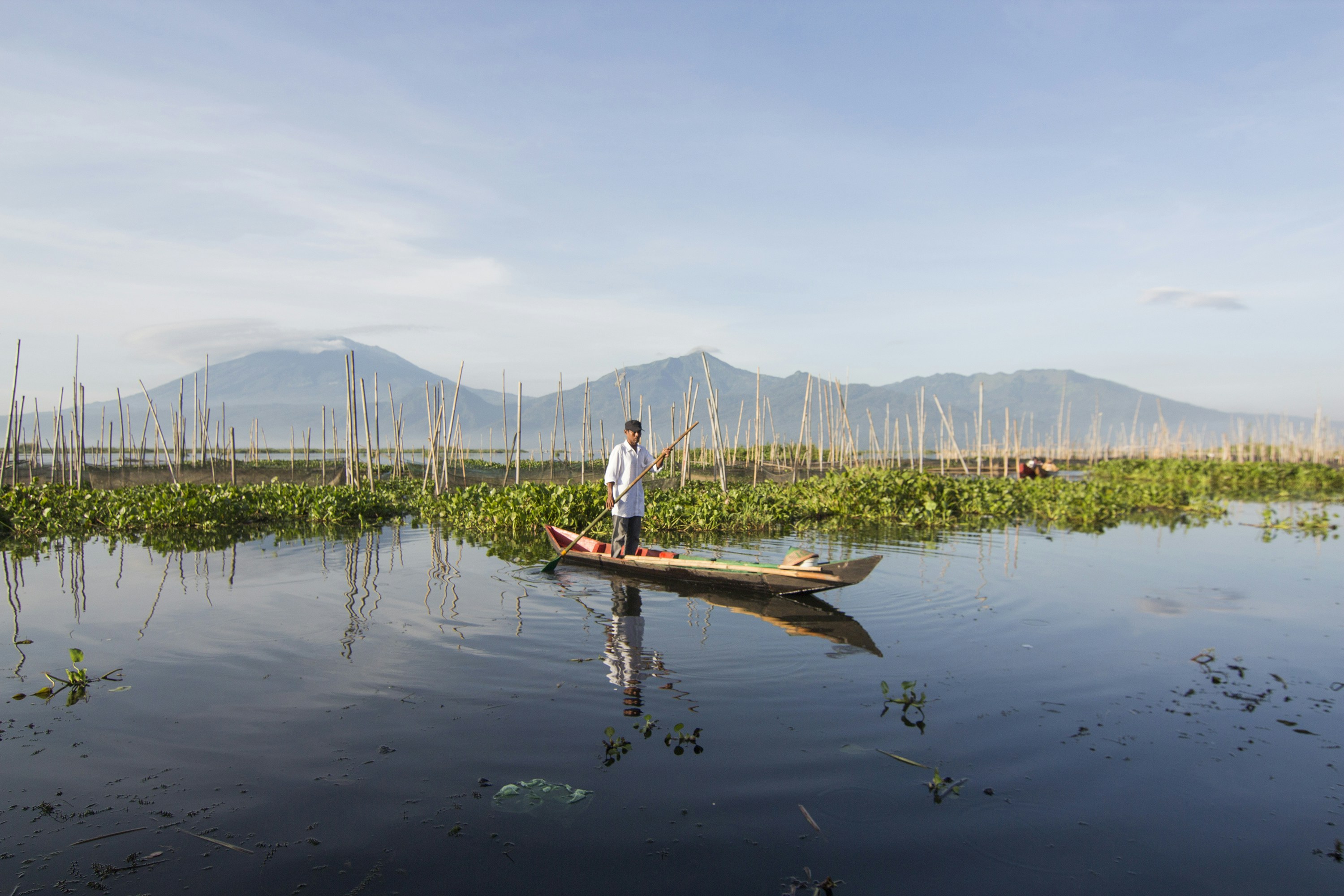 Man in a Small Boat Crossing a Serene Waterway with Distant mountains