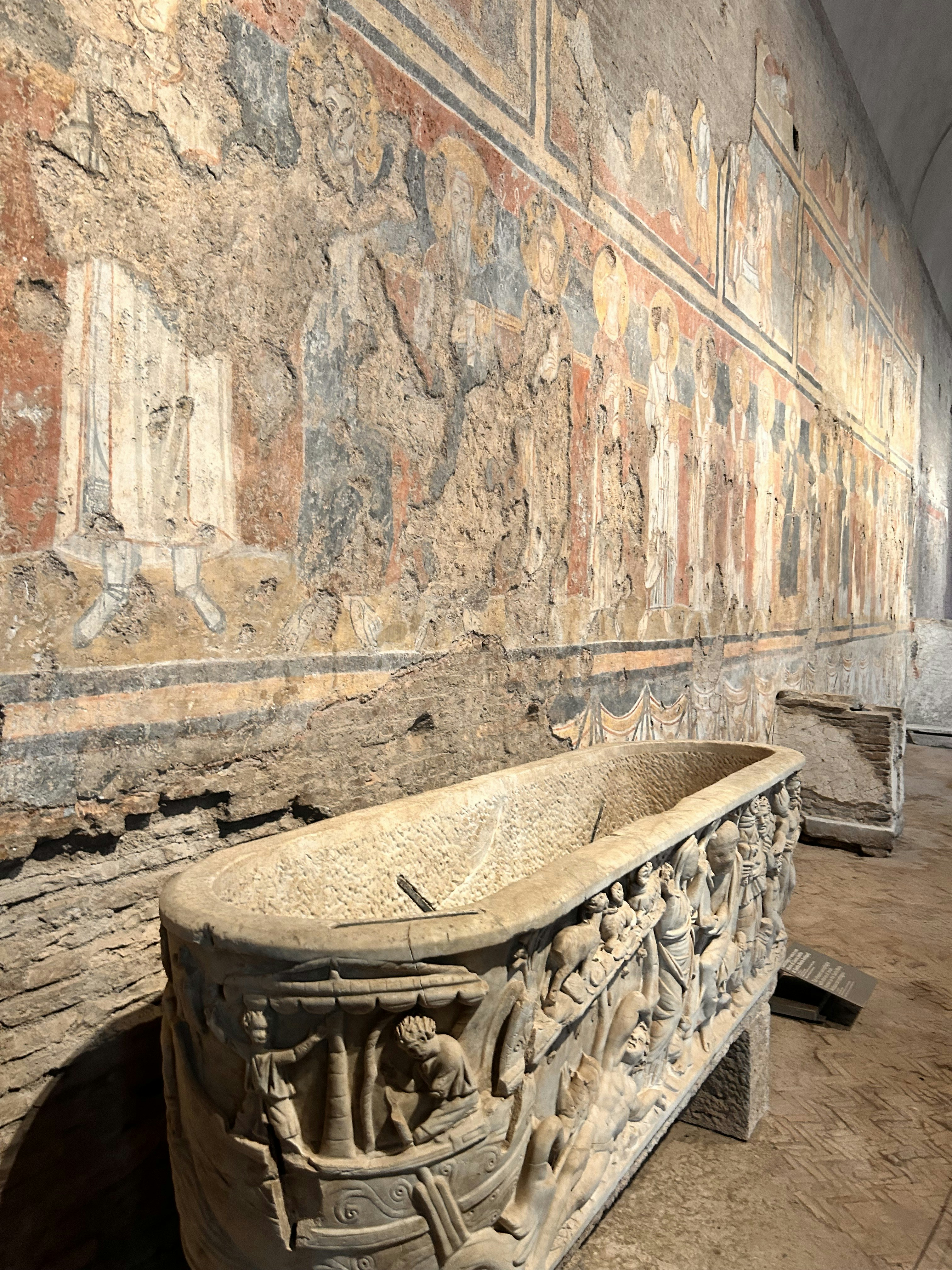 Carved sarcophagus and ancient wall frescoes in a dim tomb corridor