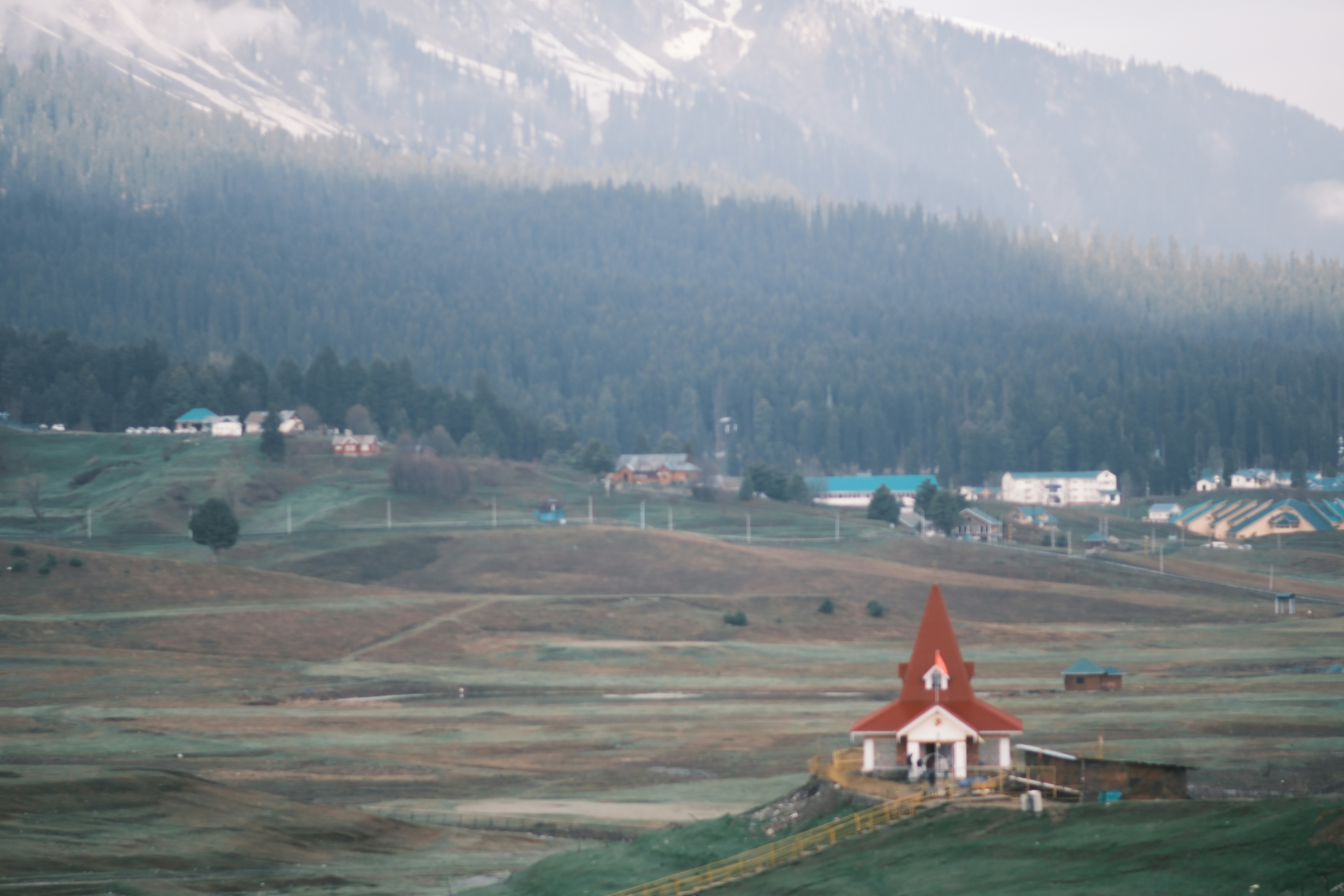 Red-roofed Chapel on rolling hills beneath a misty alpine backdrop