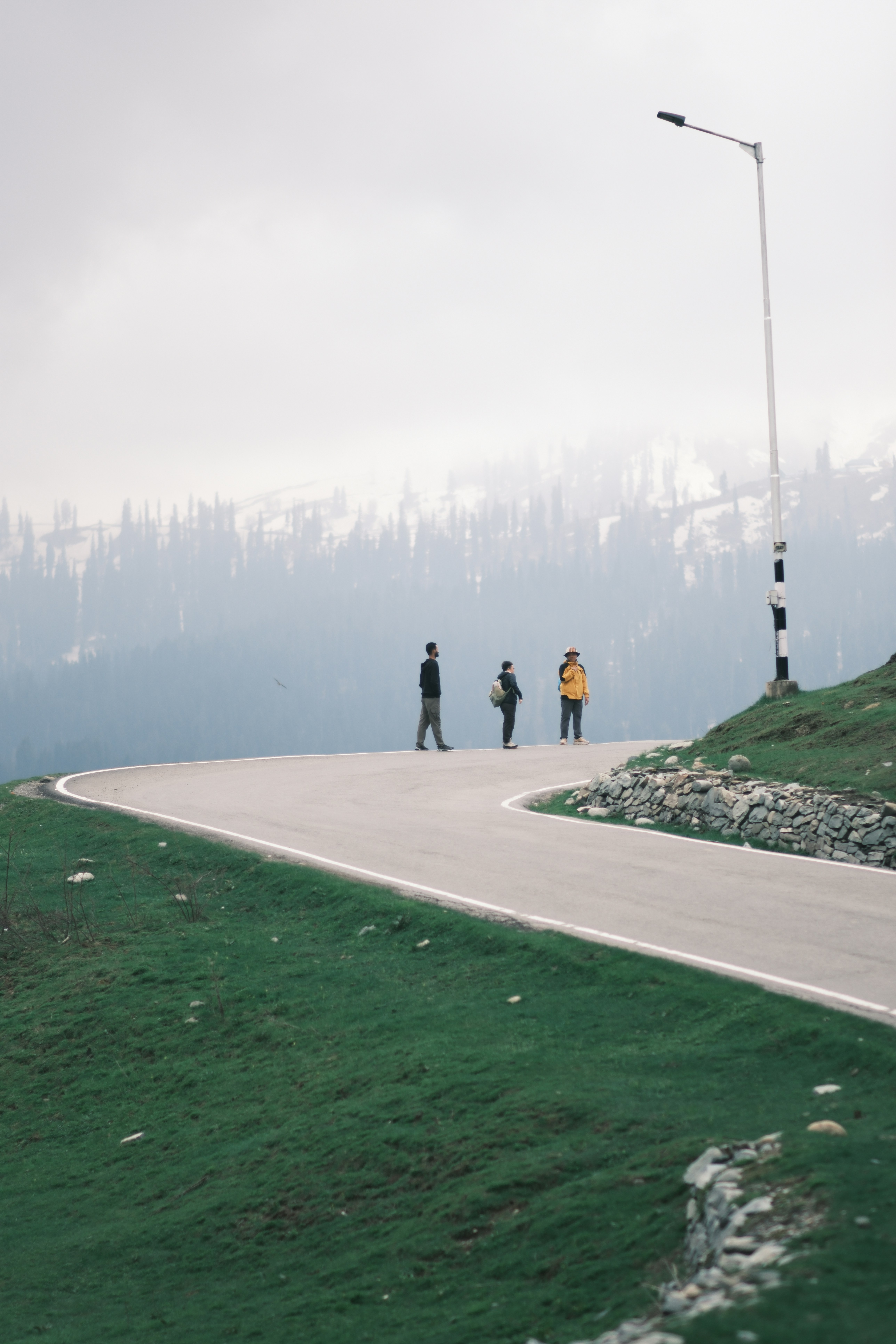 Three Wanderers on a Curving Mountain Road under a Misty Sky