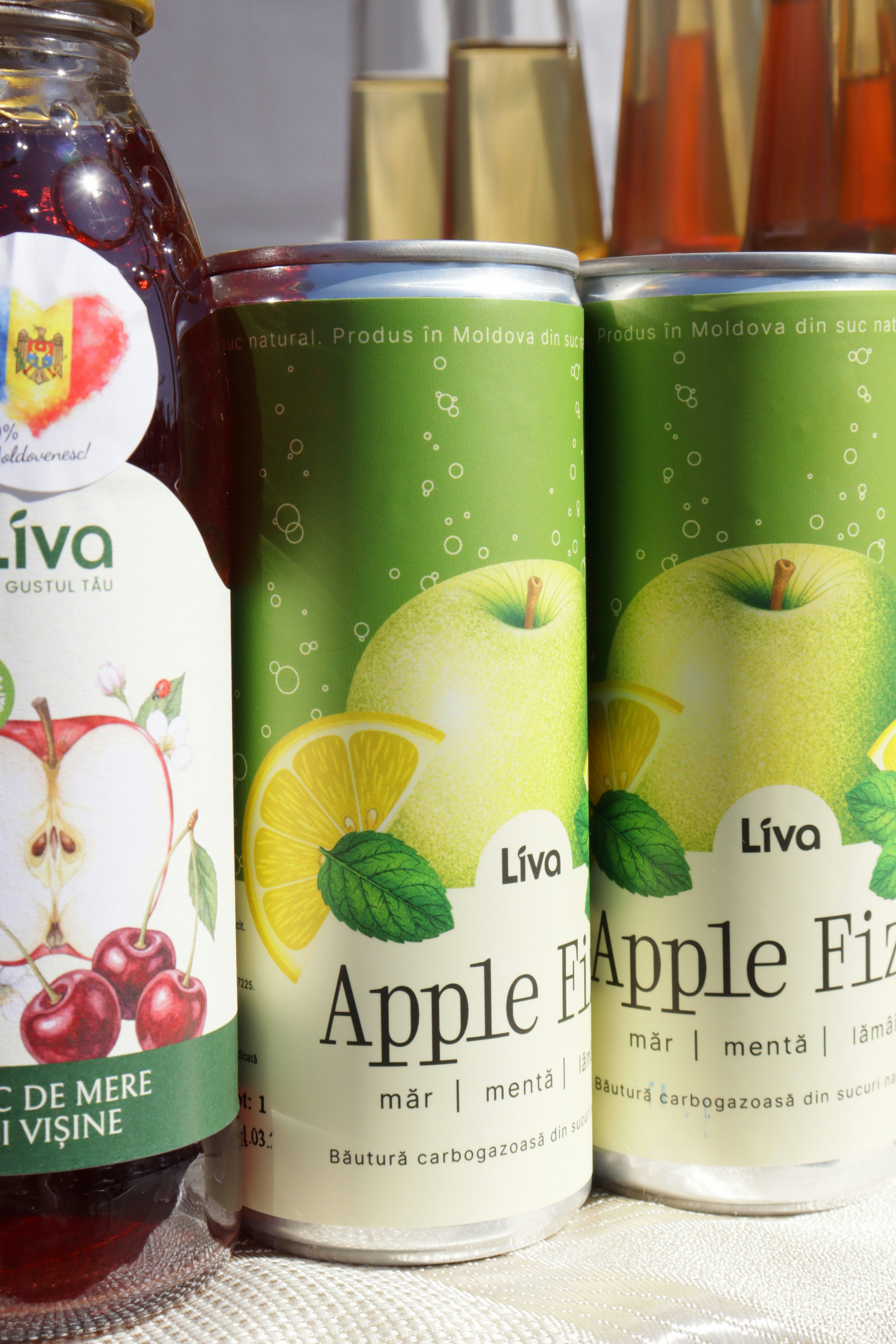 A glass bottle of red juice beside two cans of apple mint soda