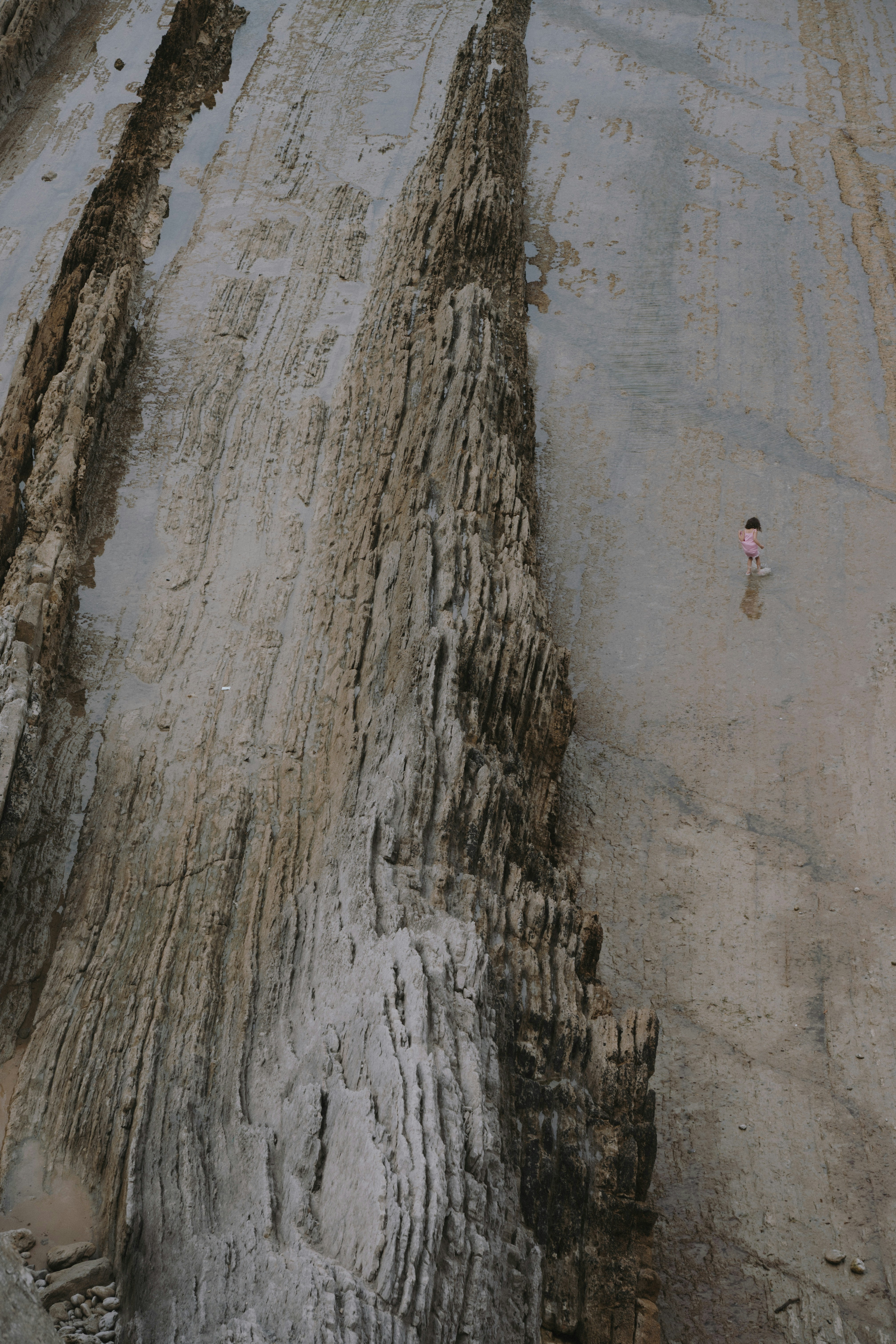 Gigantic coastal cliff carved by time, with a lone child near the waterline