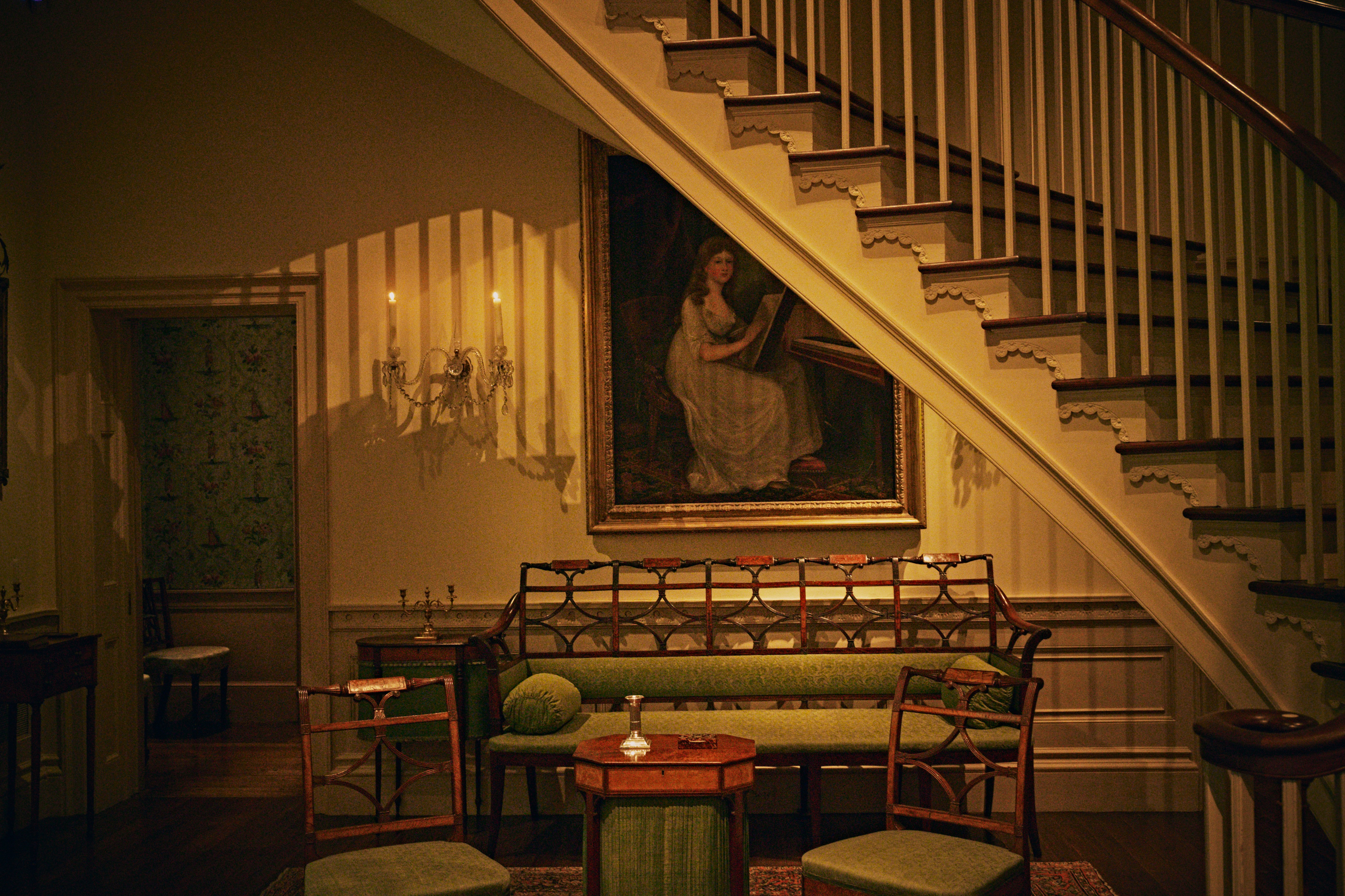 Dimly Lit Parlor: Vintage Seating Beneath a Staircase Portrait