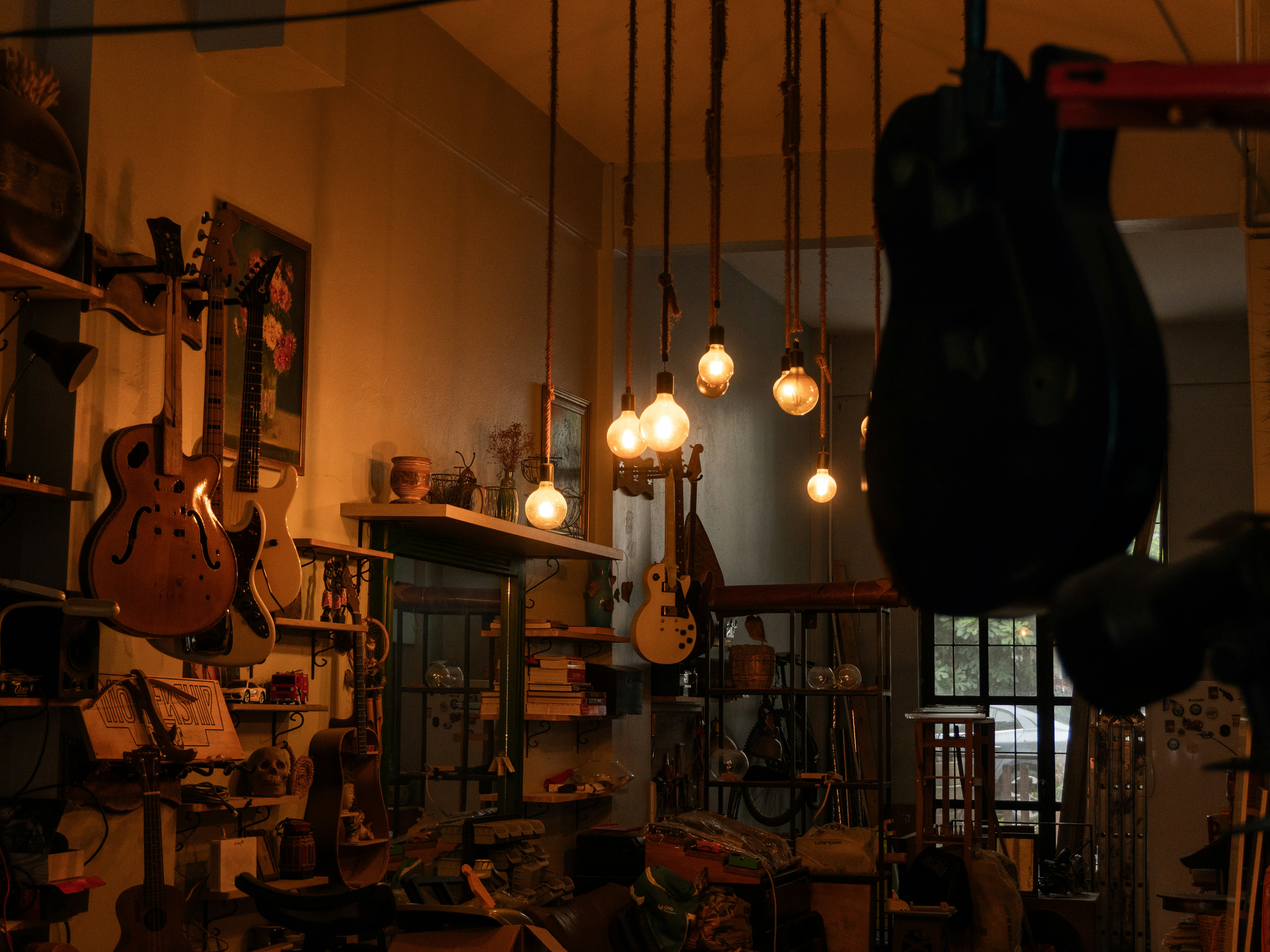 Warm guitar shop interior with multiple guitars on walls and shelves, a hanging bulb chandelier, captured with moody lighting and a shallow depth of field.