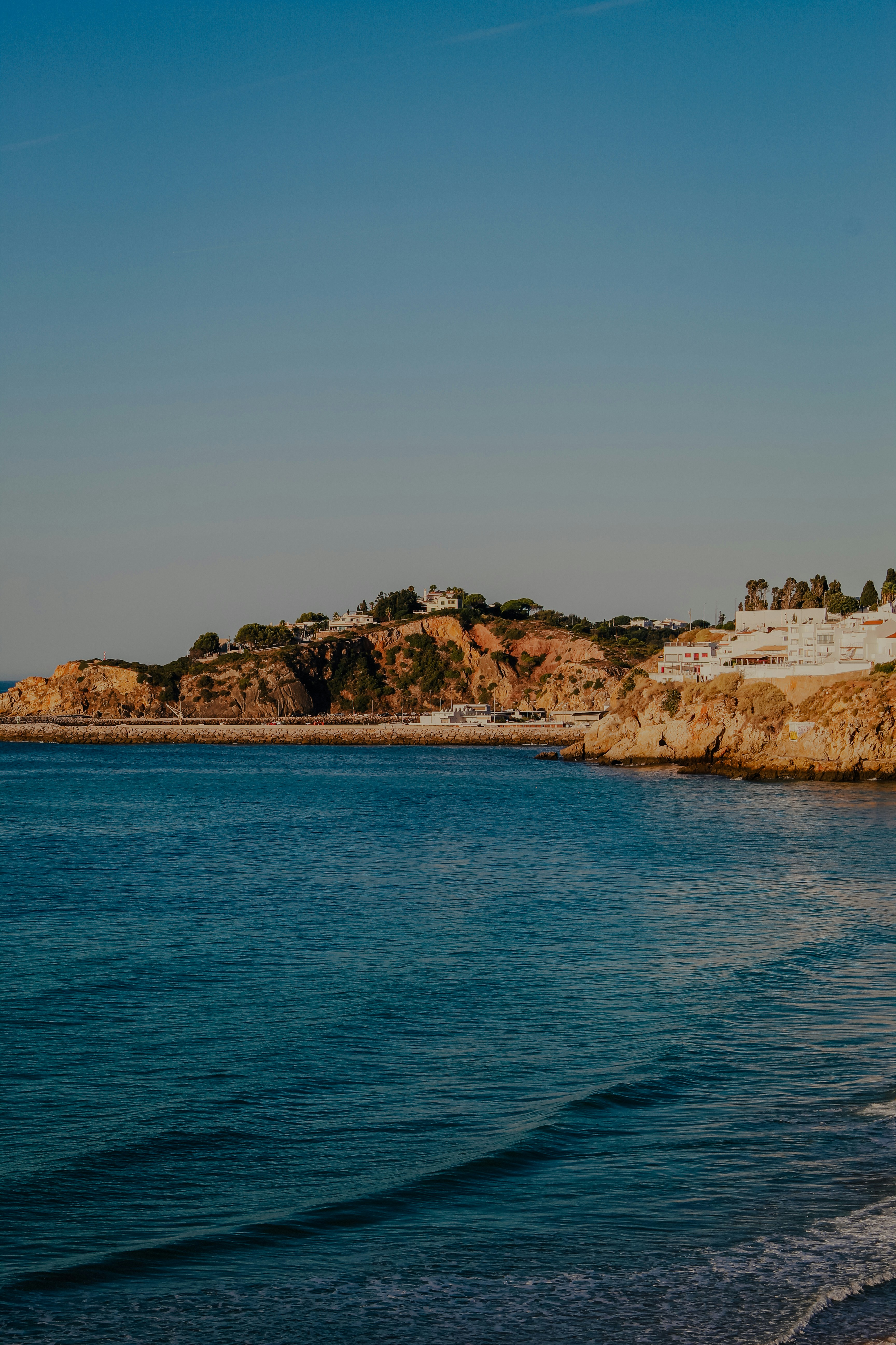 Cliffside Harbor: Sunlit Buildings Above Quiet Waters