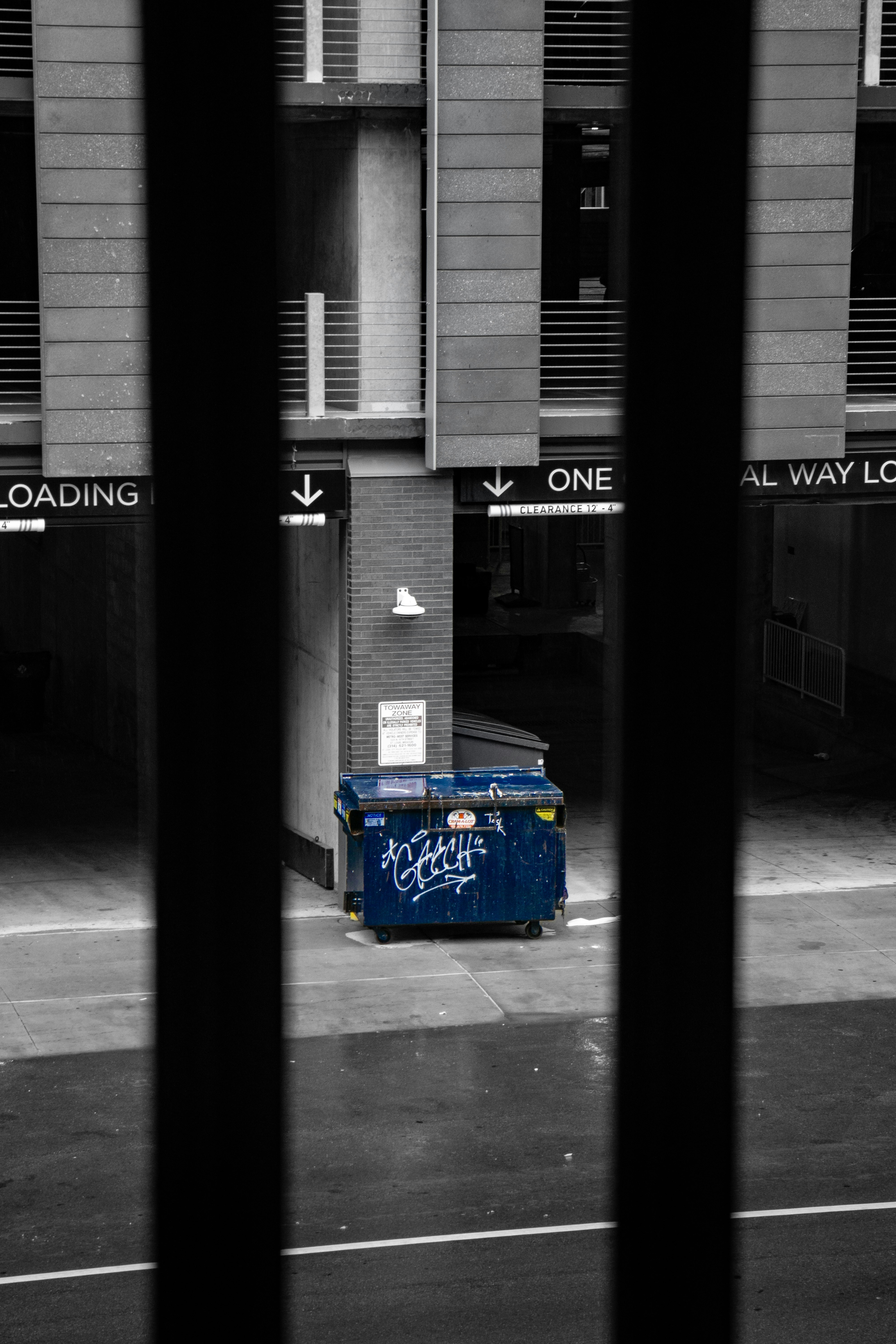 Blue Dumpster in a Narrow City Corridor Seen Through Vertical Slats
