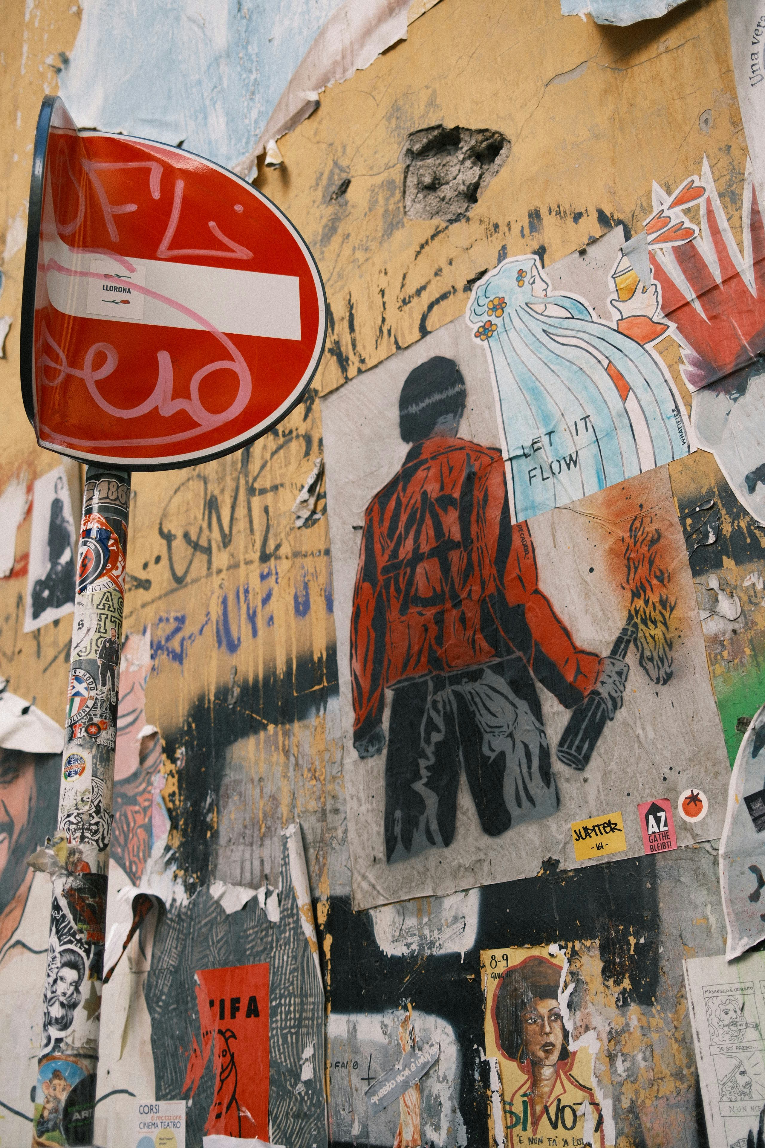 A red no entry sign beside a wall covered in layered street art posters