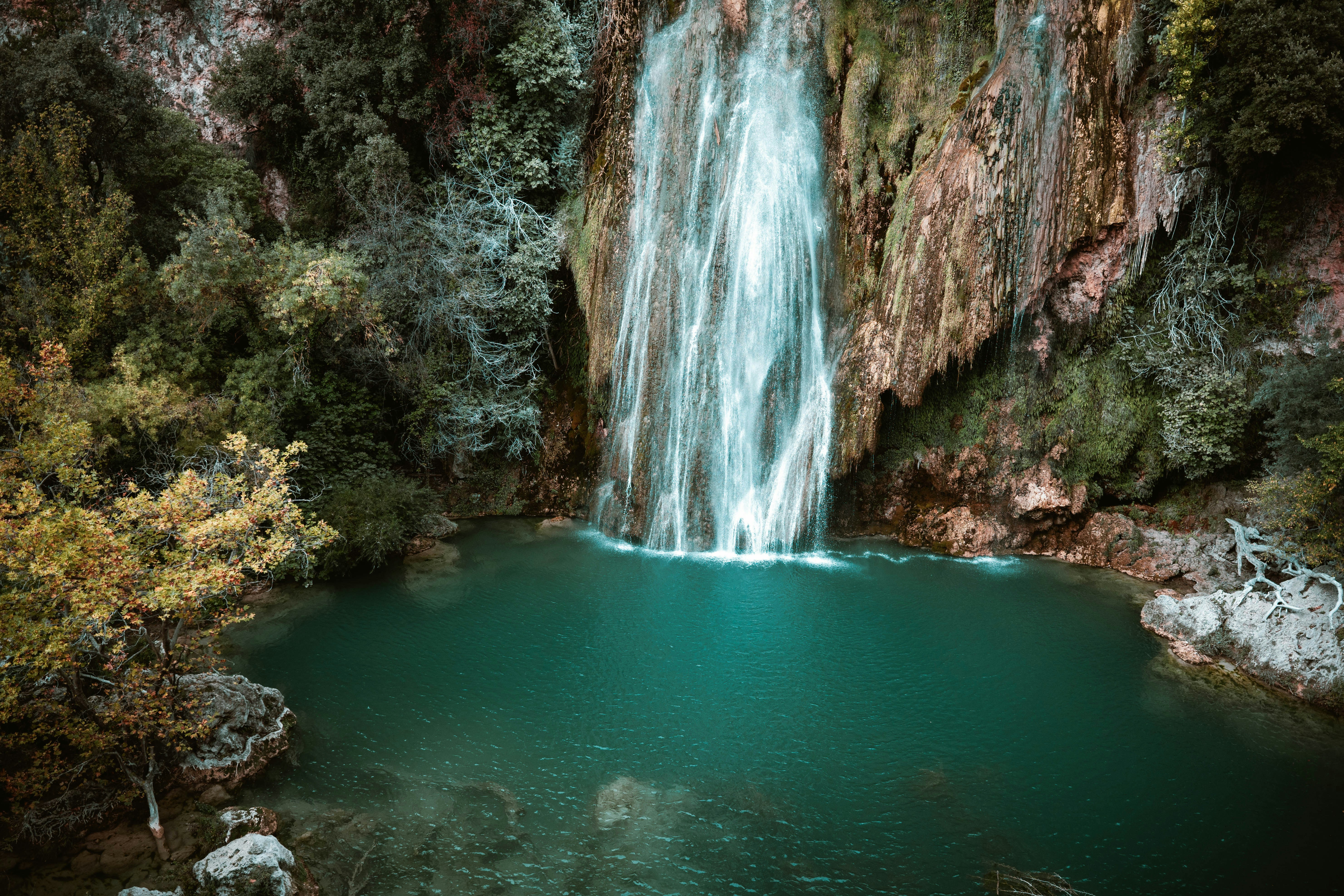 Emerald Cascade: Aerial View of a Narrow Waterfall Plunging into Teal Pool