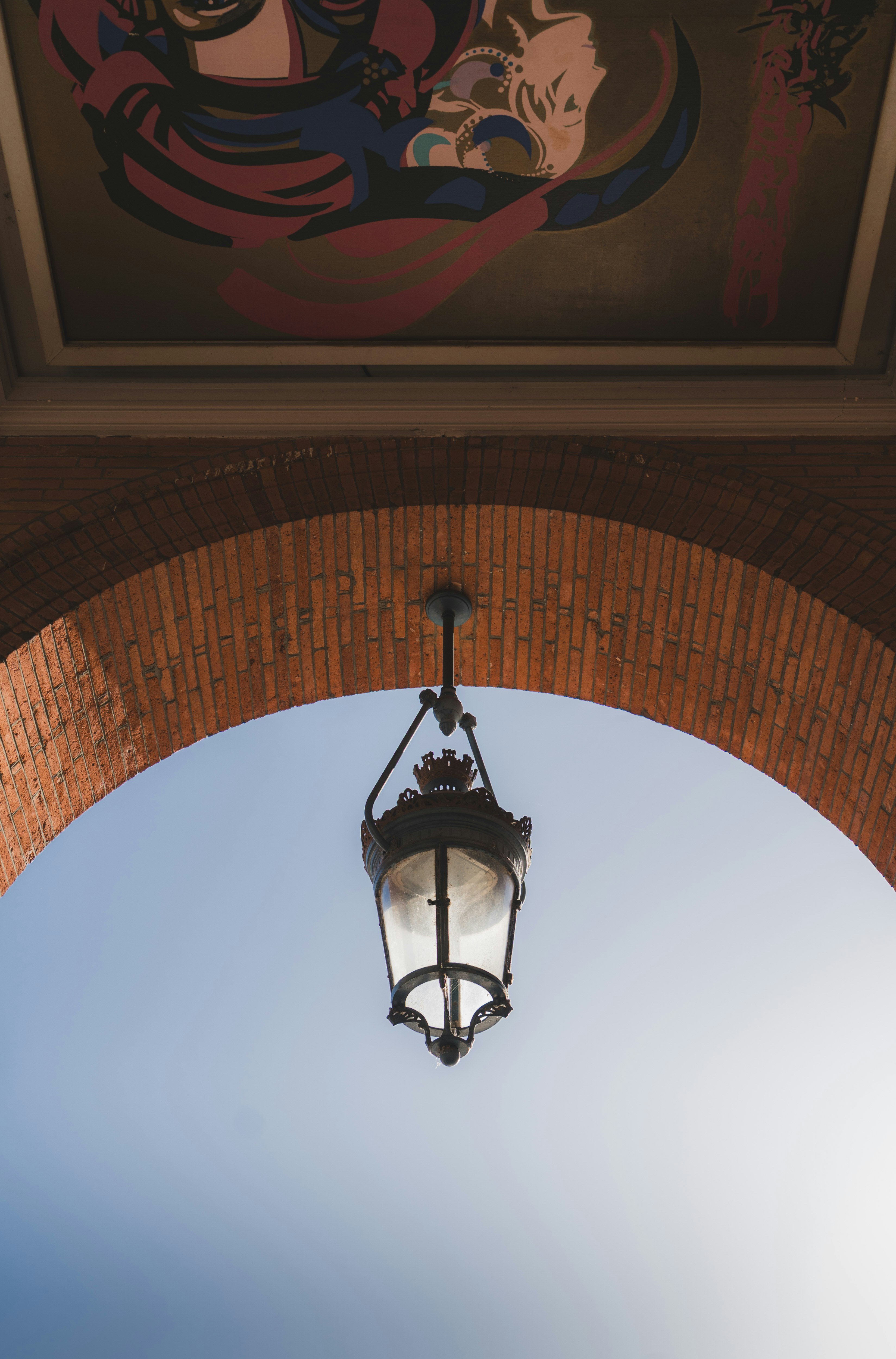 A hanging lantern suspended under a brick archway with a painted ceiling
