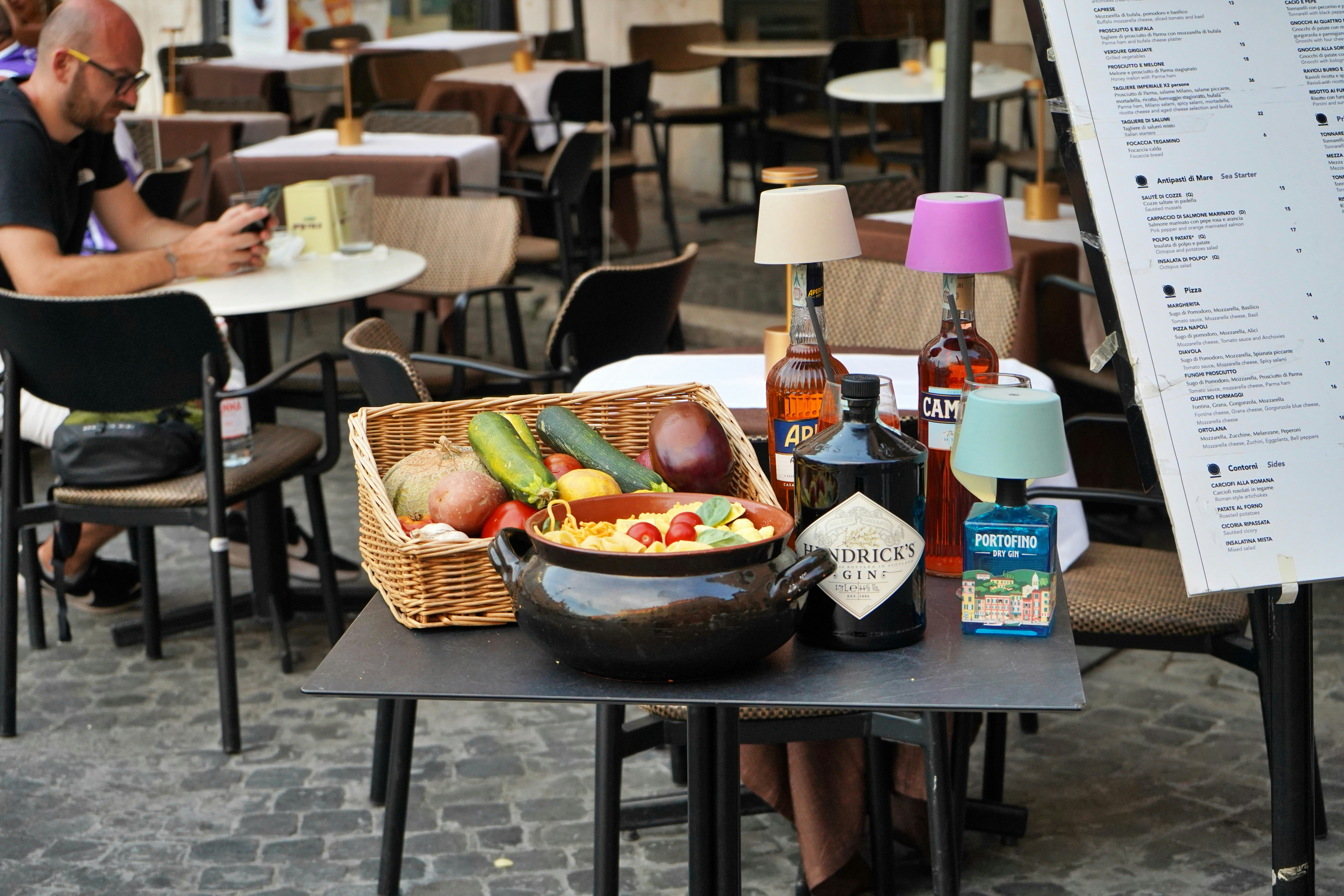 Market Table on Cobblestones: A Basket of Produce and Beverages Amid Café Patrons