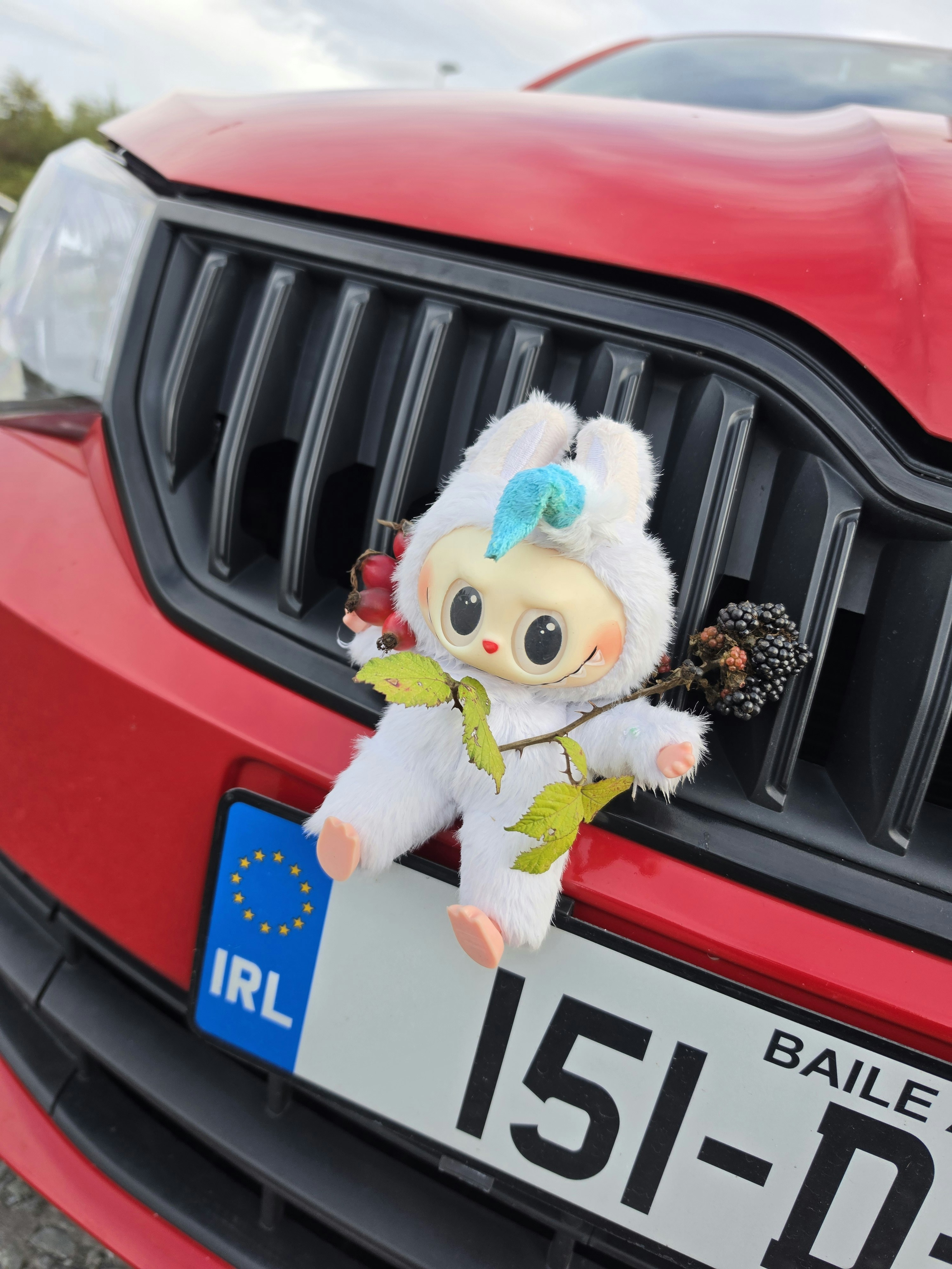 Tiny Plush on Chrome Grille: A Cheerful Toy Dangles from the Front of a Red Car