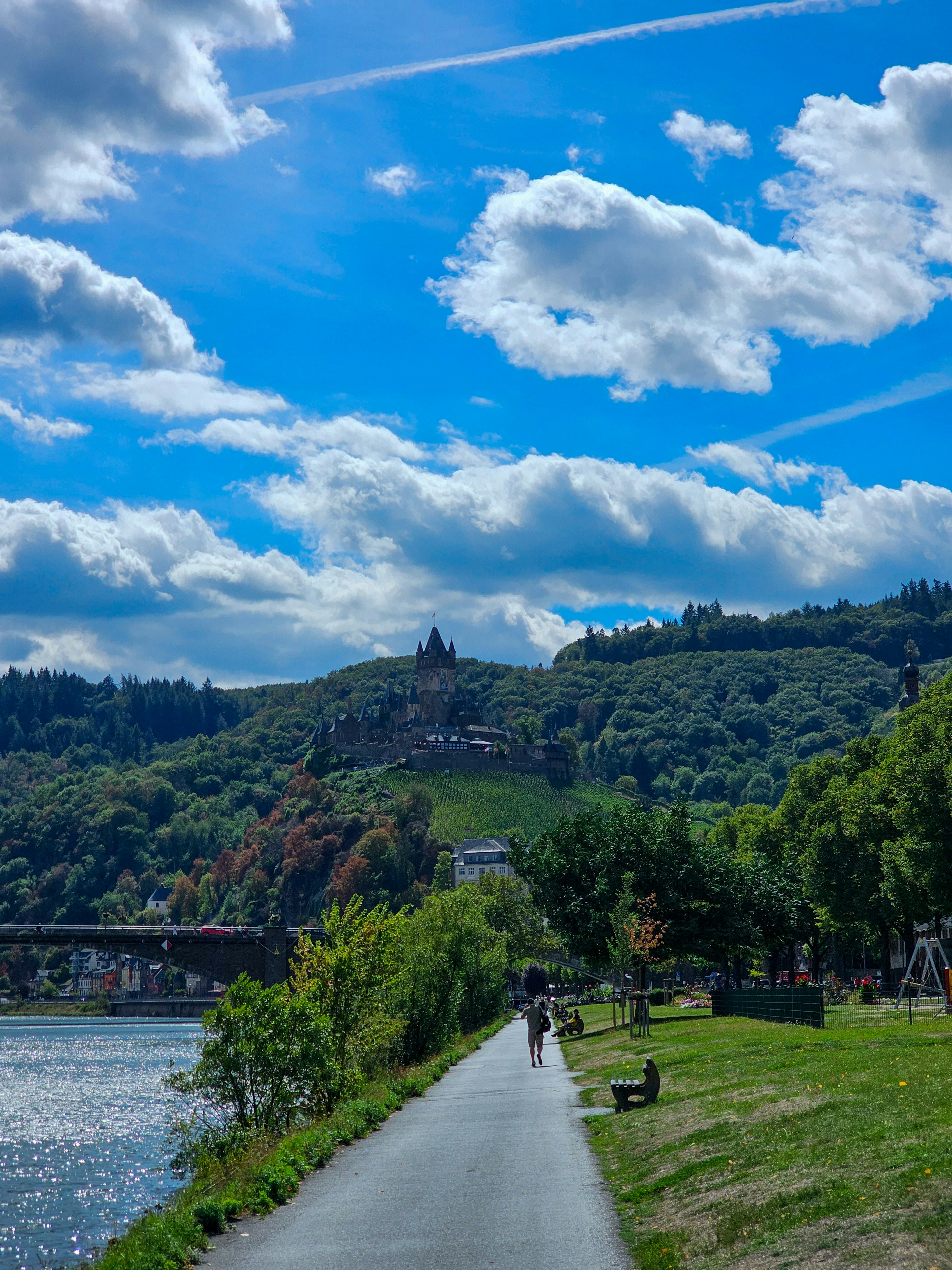 Riverside Path Toward a Hillside Village Under Blue Skies