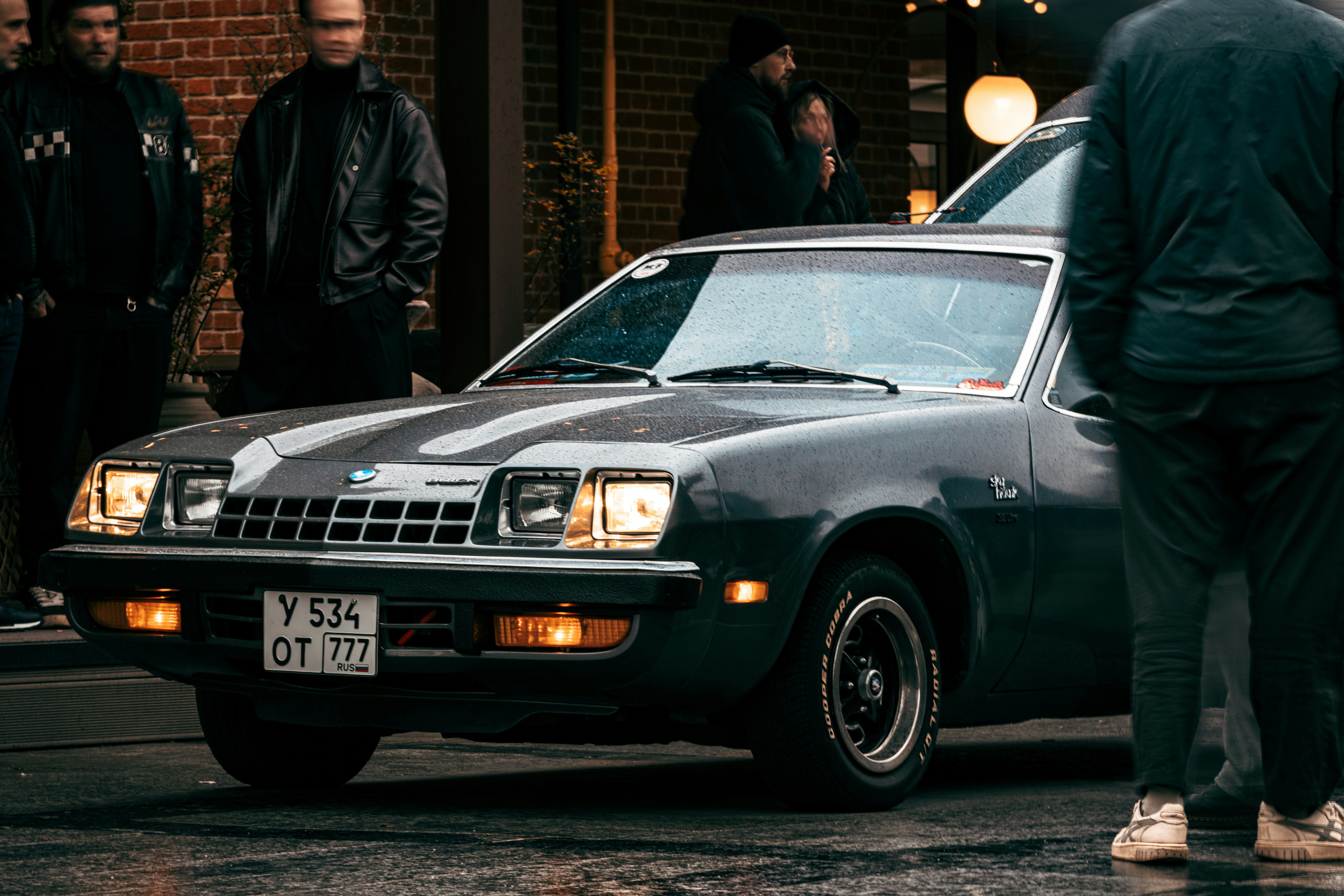 Vintage sedan under streetlight glow with onlookers in the background