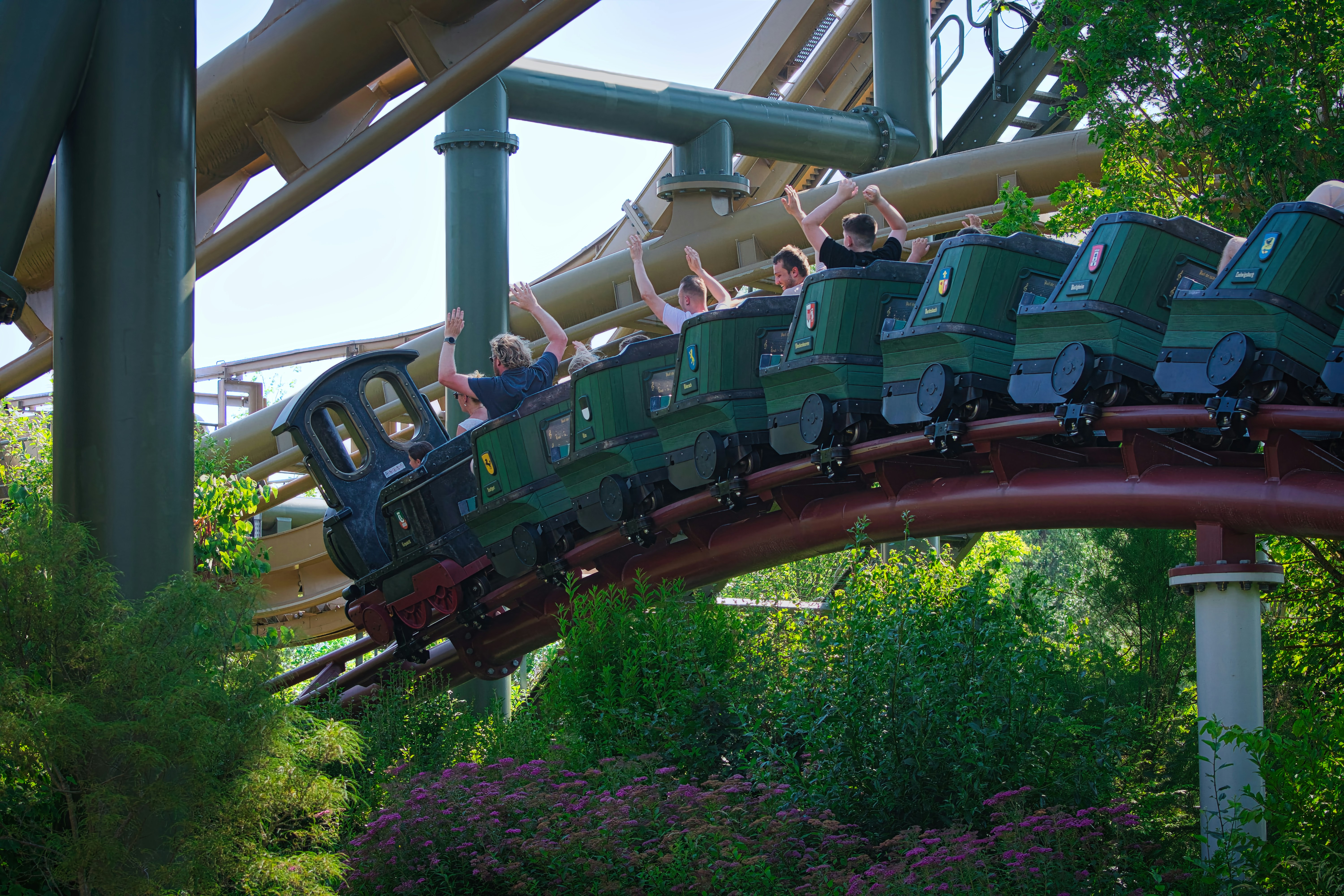 Lifting Moment: A Green Rollercoaster Train Rushing Through Sunlit Tracks