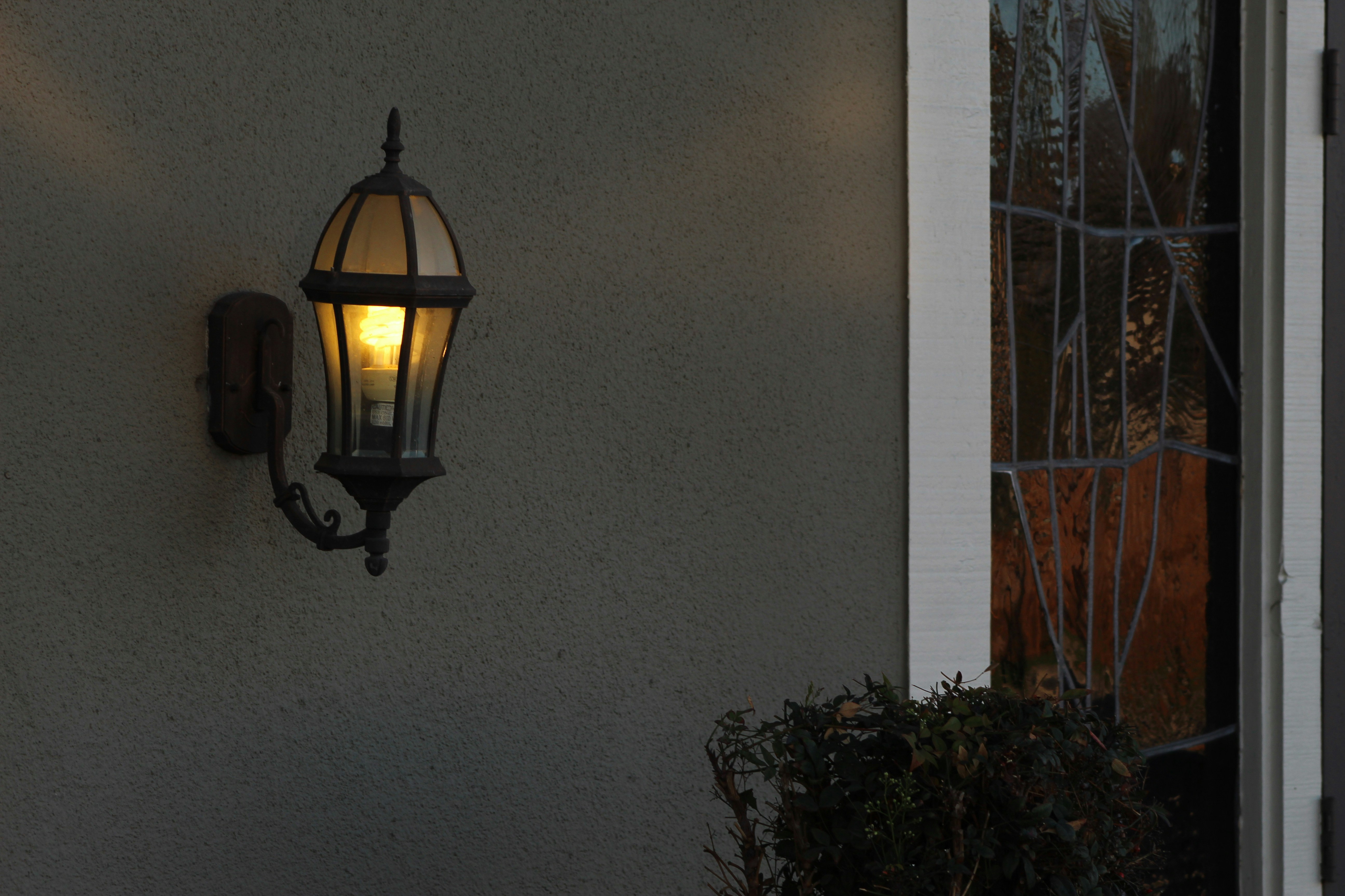 A glowing wall lantern mounted on a grey stucco wall beside a glass door