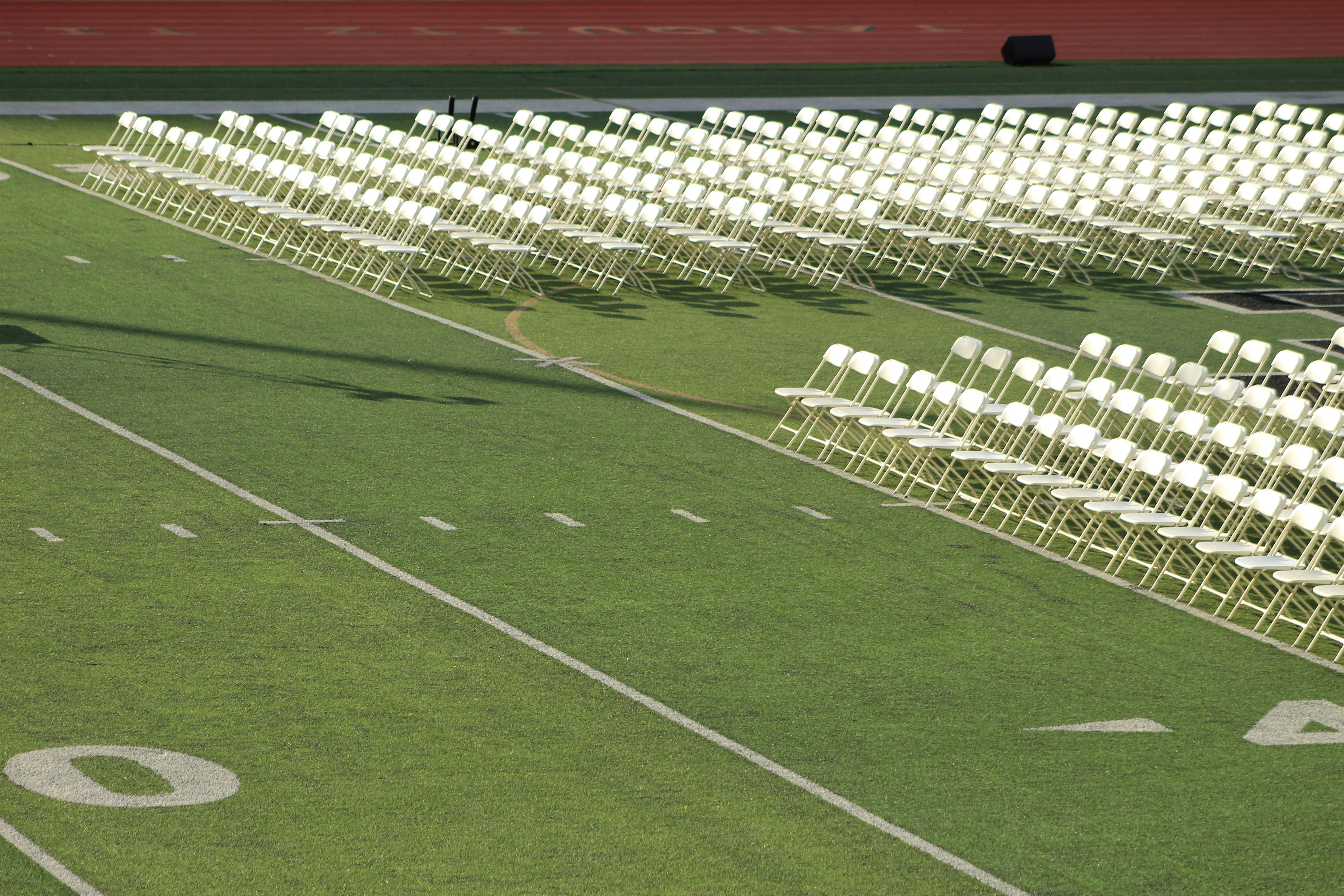Rows of empty stadium chairs casting long shadows across a green field