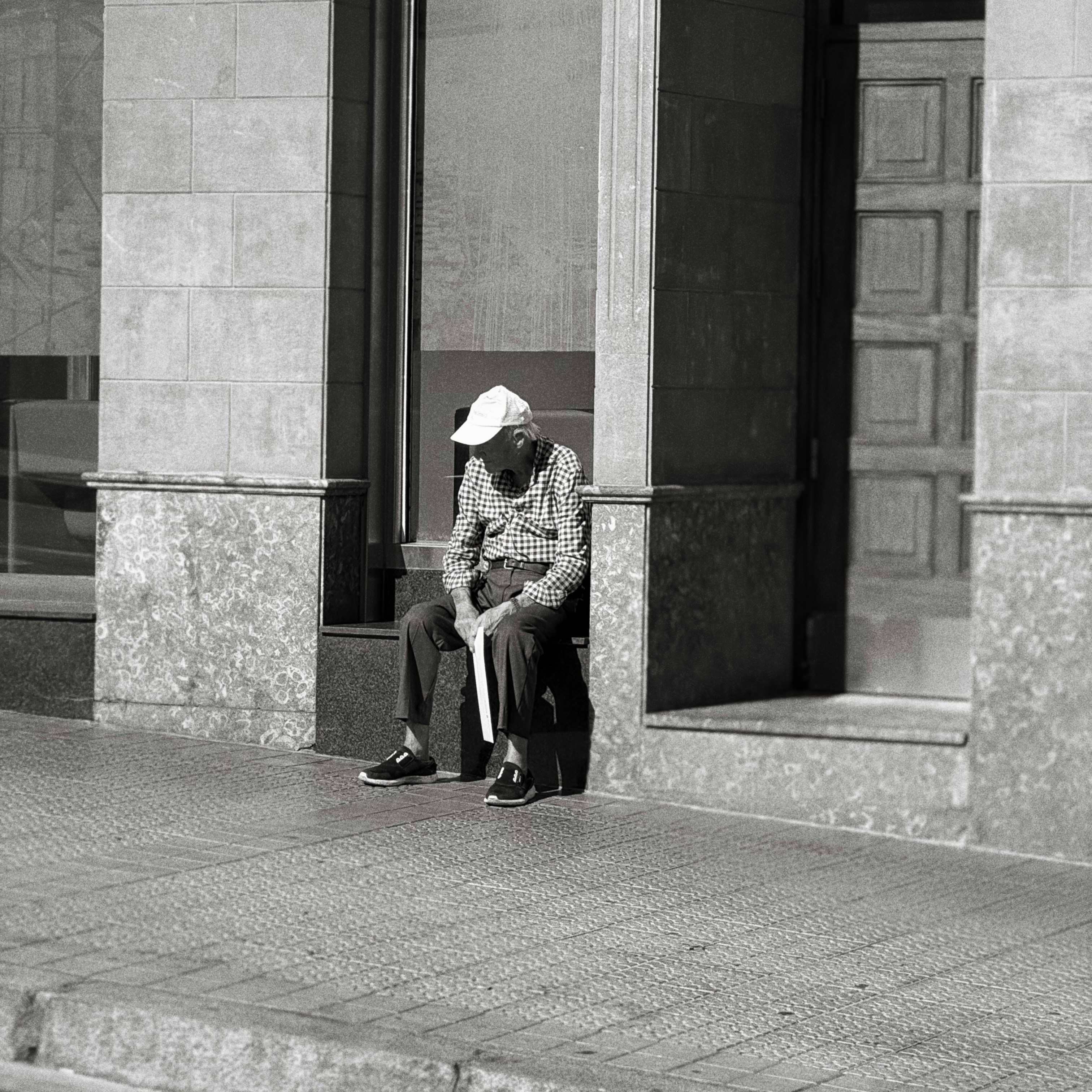 Seated in Shadow: A Quiet Moment Outside a Stone Facade