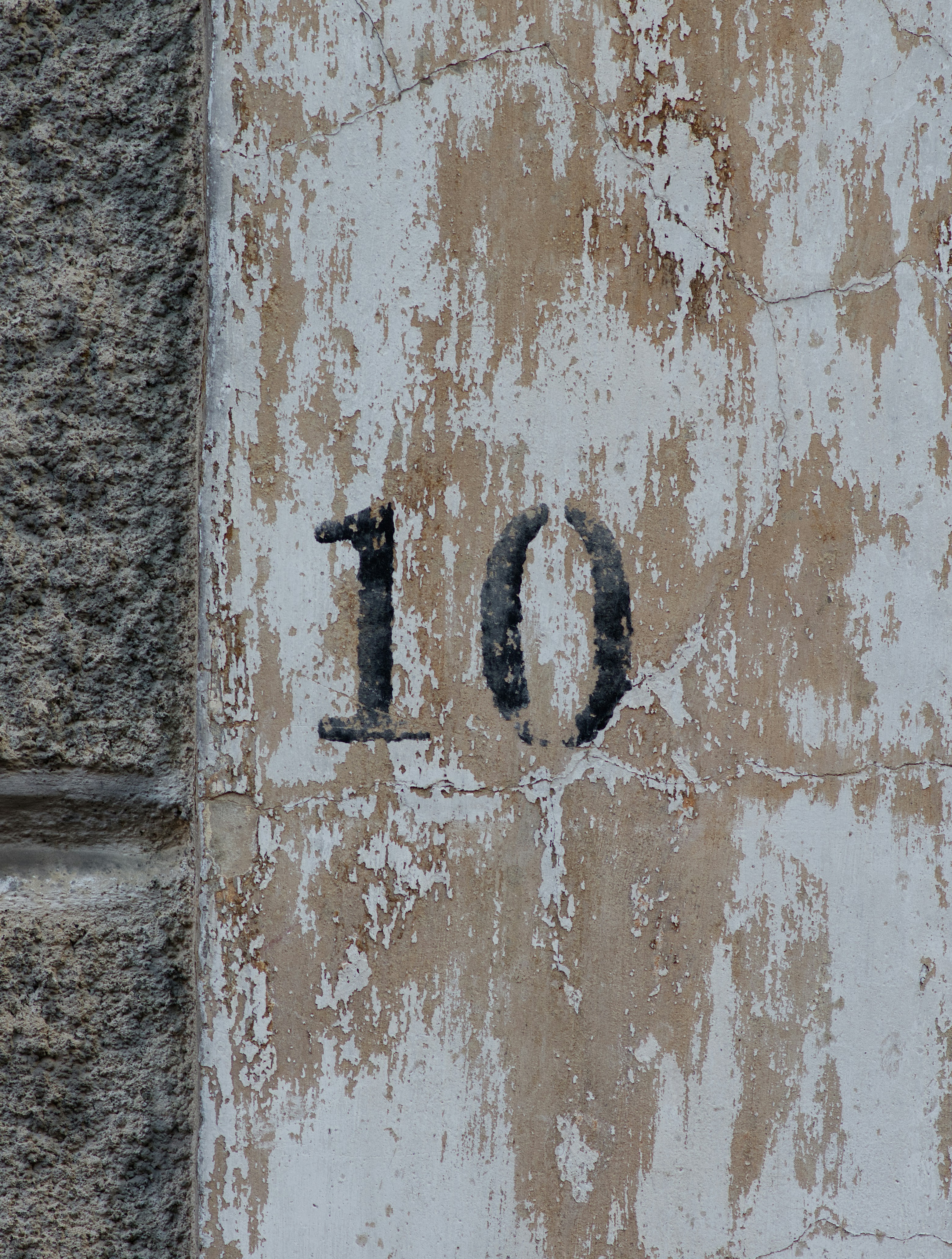 Weathered wall with the number 10 faded into peeling plaster, a study in texture and color. This is a tactile close-up suitable for urban texture photography.