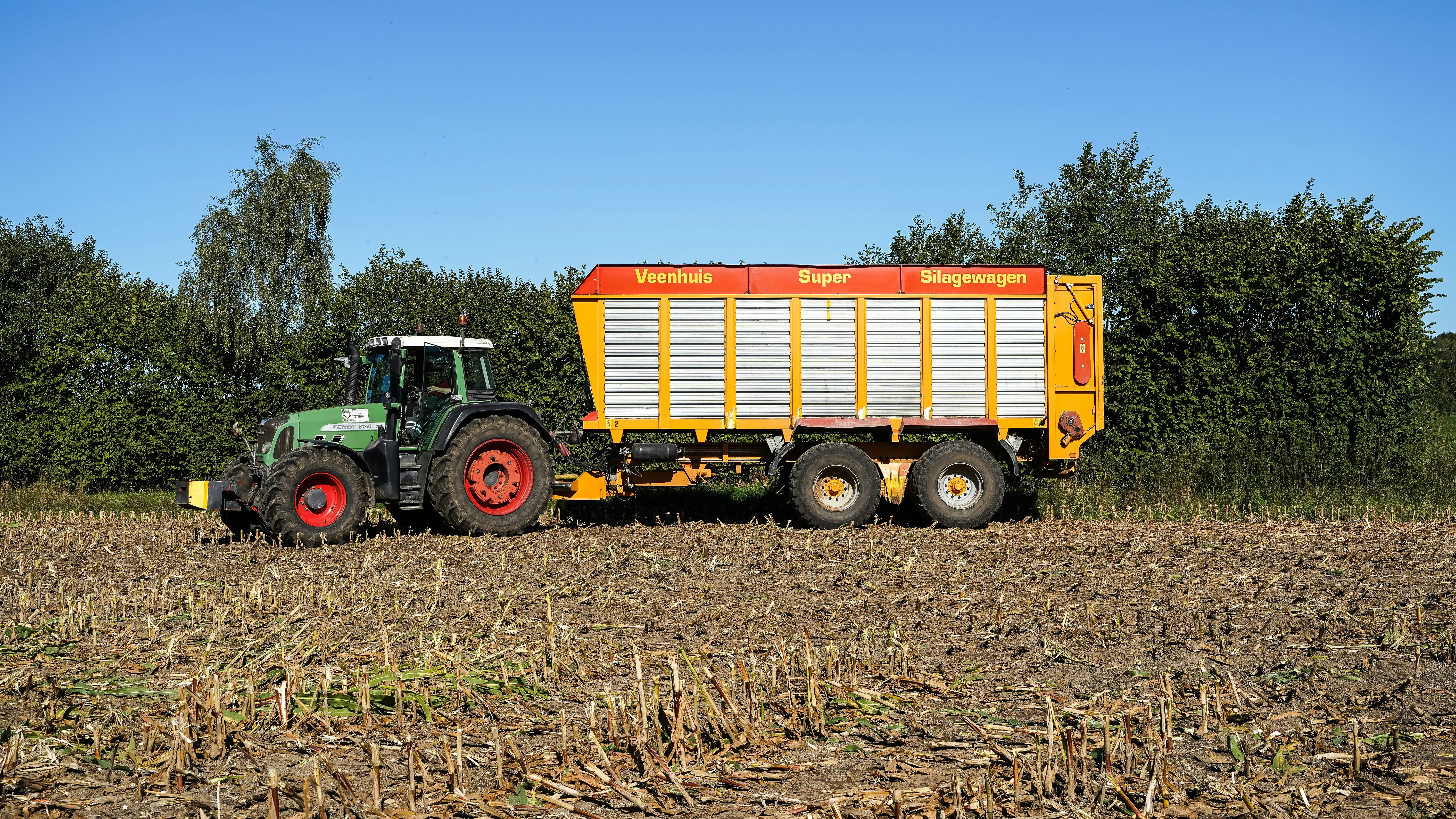 Harvest Drive: Green Tractor Pulling Orange Farm Trailer Across Sunlit Field