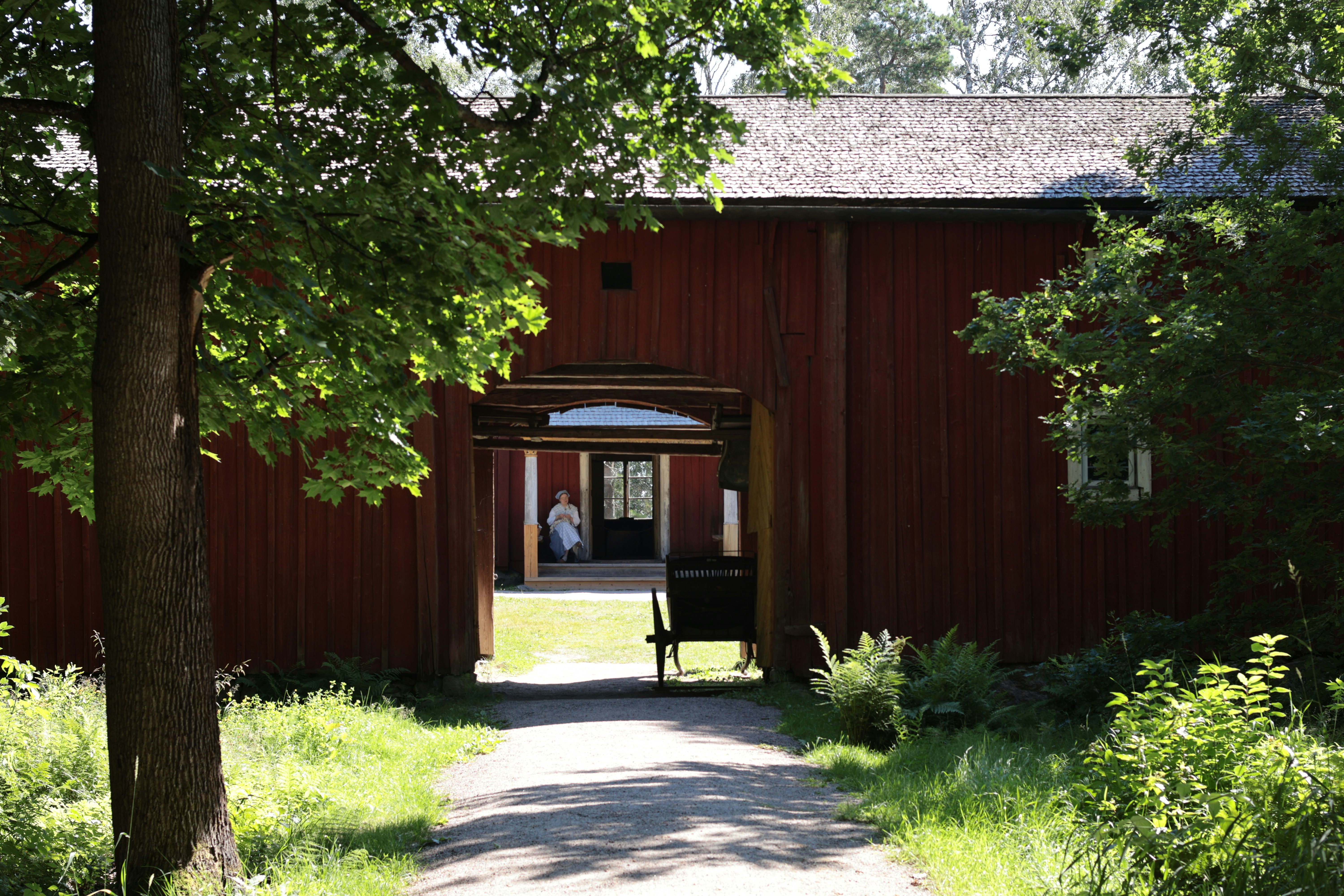 Sunlit Archway: A Red Barn Path to the Quiet Farmyard