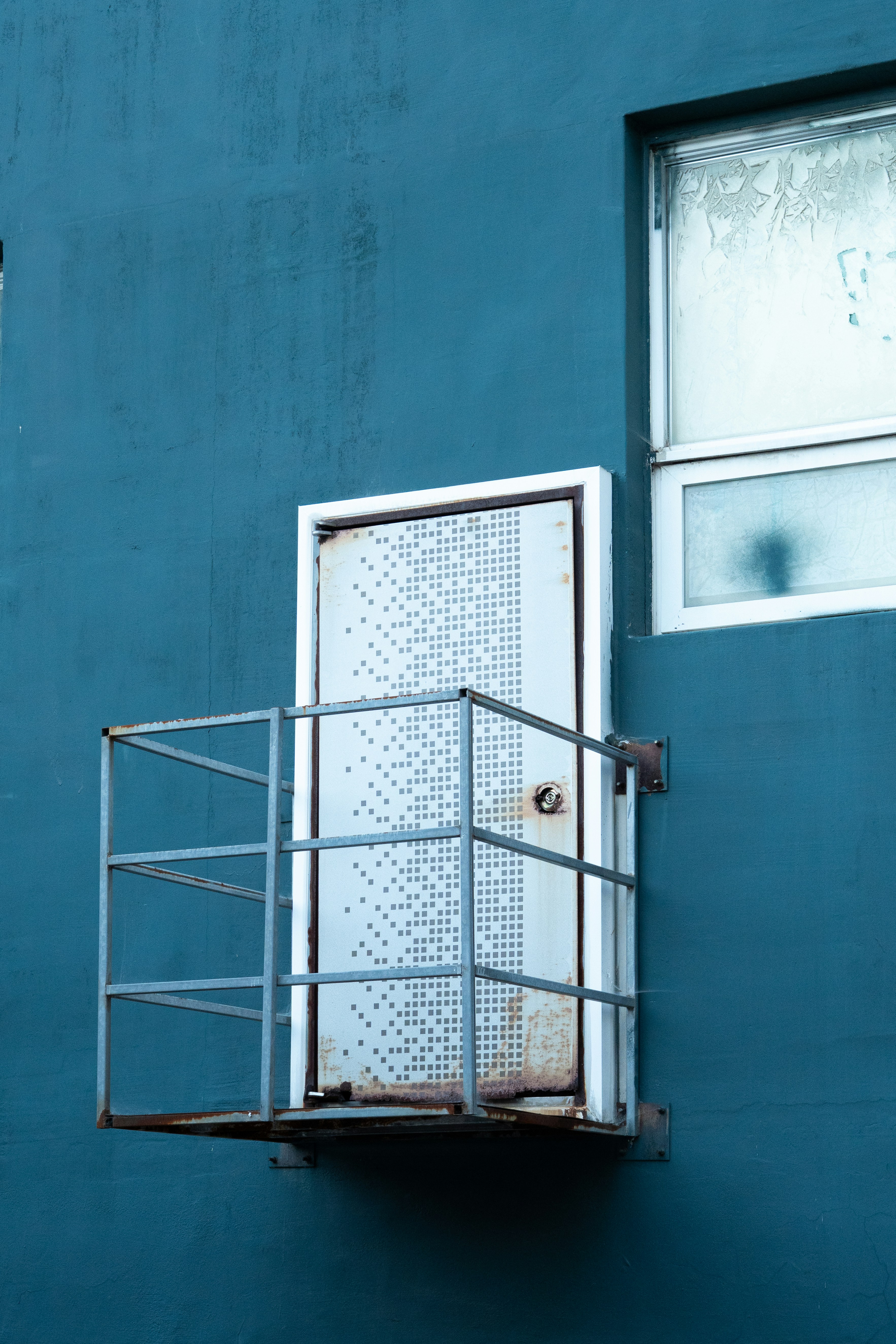 Blue Facade with Rusted Balcony and Perforated Door